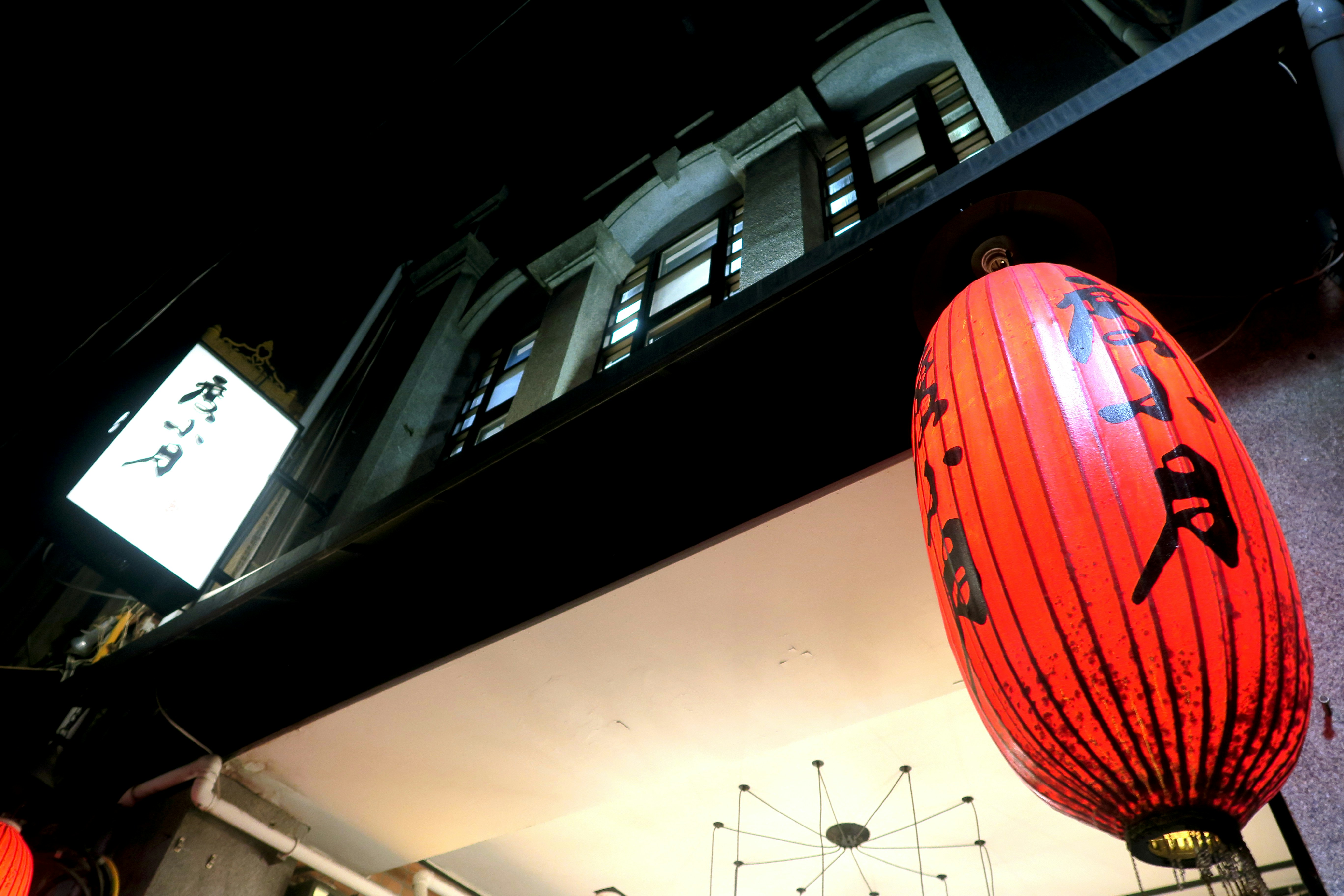 Red lantern hanging under a building's facade, illuminated against a dark city night.