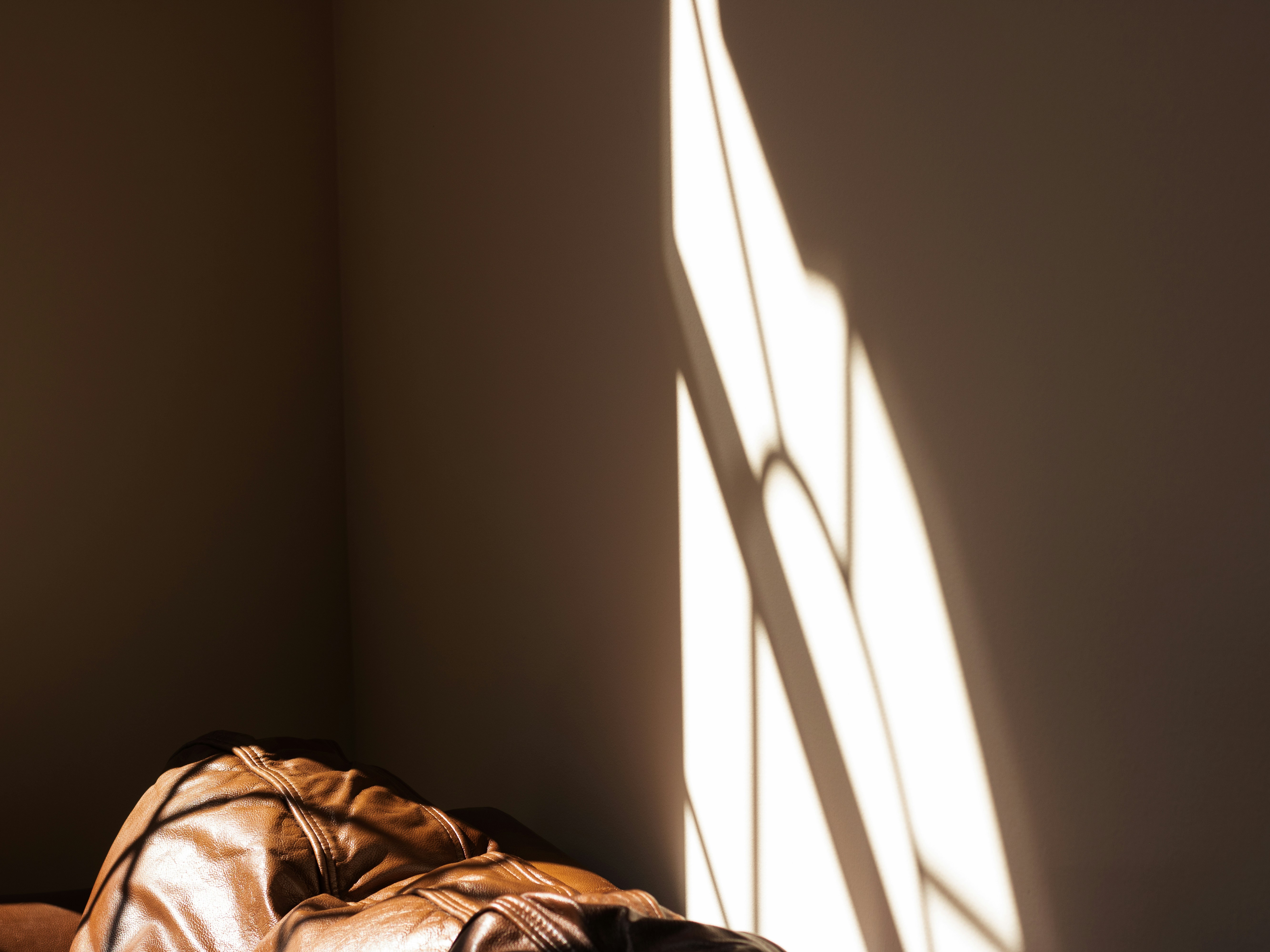 Warm leather couch partially illuminated by soft shadows cast on a neutral wall.
