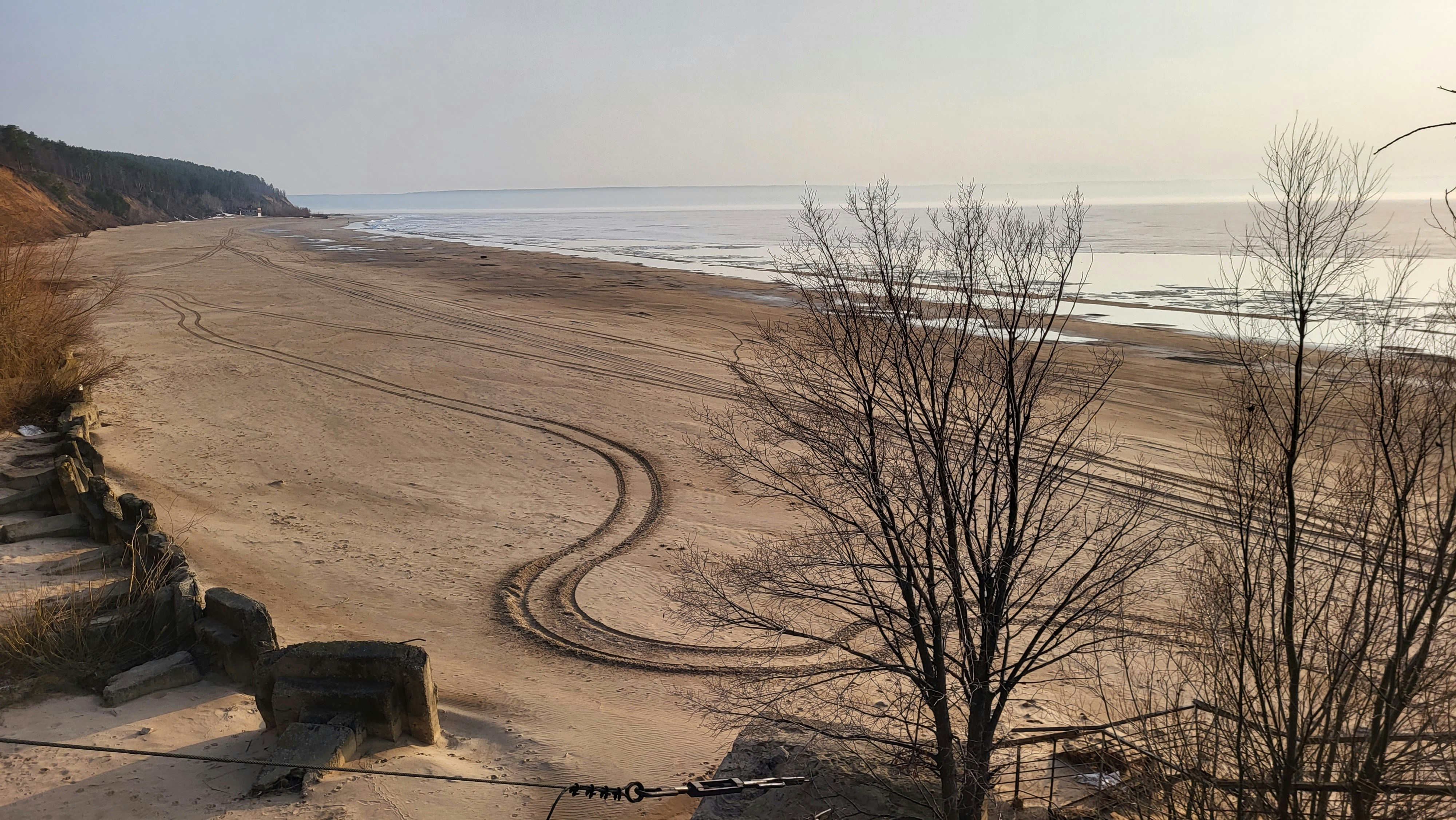 Curved Tire Trails Lead the Quiet Sea on a Wind-Swept Beach