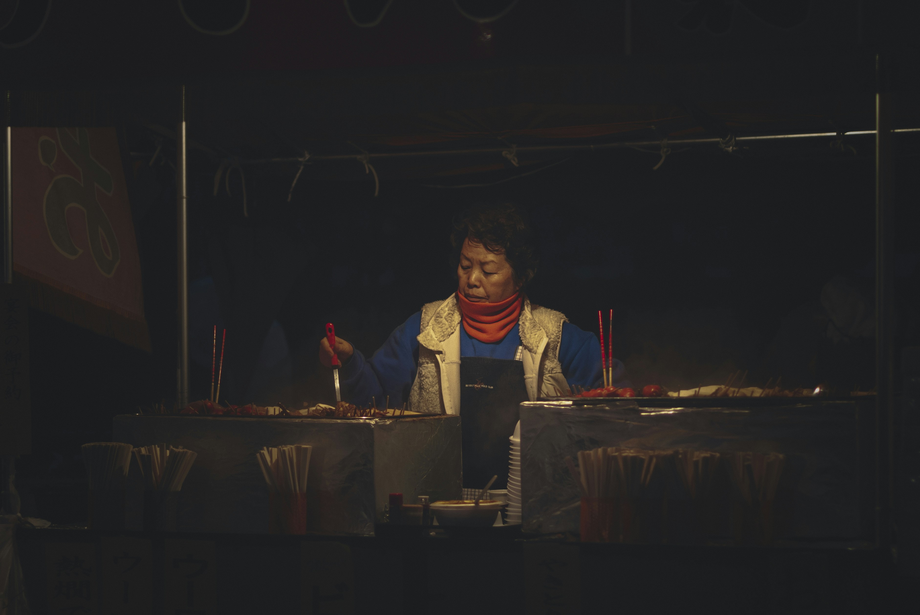 Street vendor preparing food at a dimly lit stall in Tokyo.