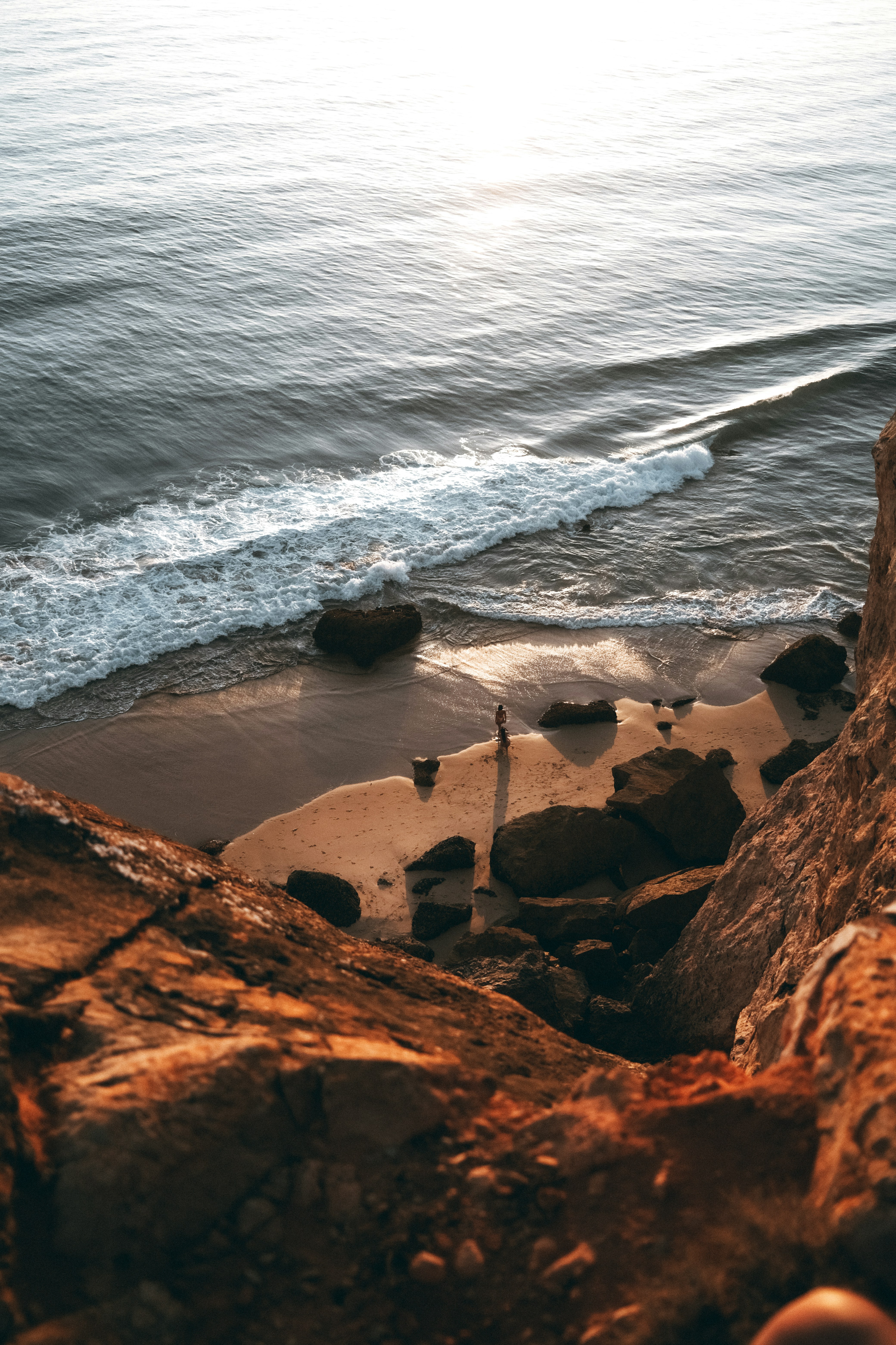 Waves gently lap against a sandy beach framed by rocky cliffs, capturing the serene essence of the coastline at sunset.