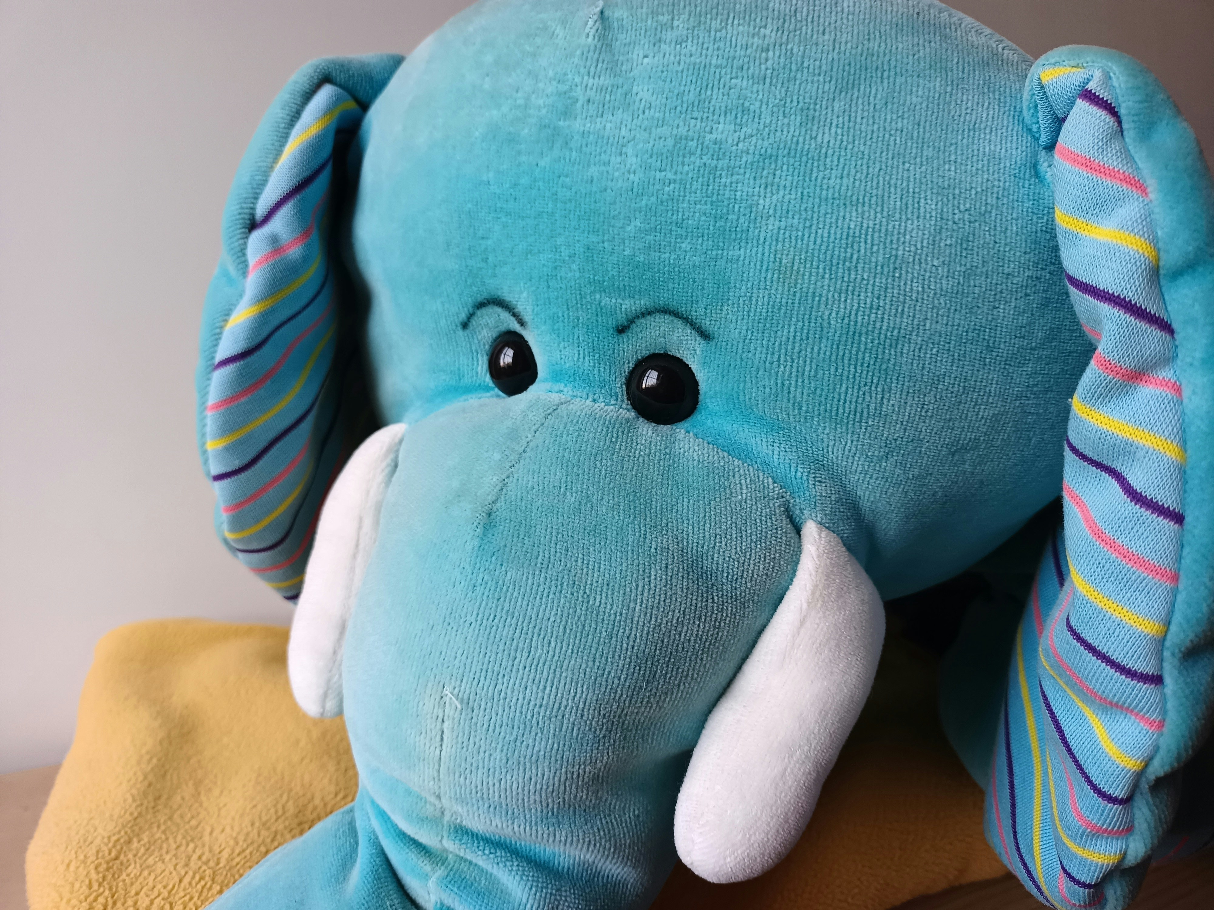 A blue plush elephant, with black eyes and stripey ears. White and yellow background.