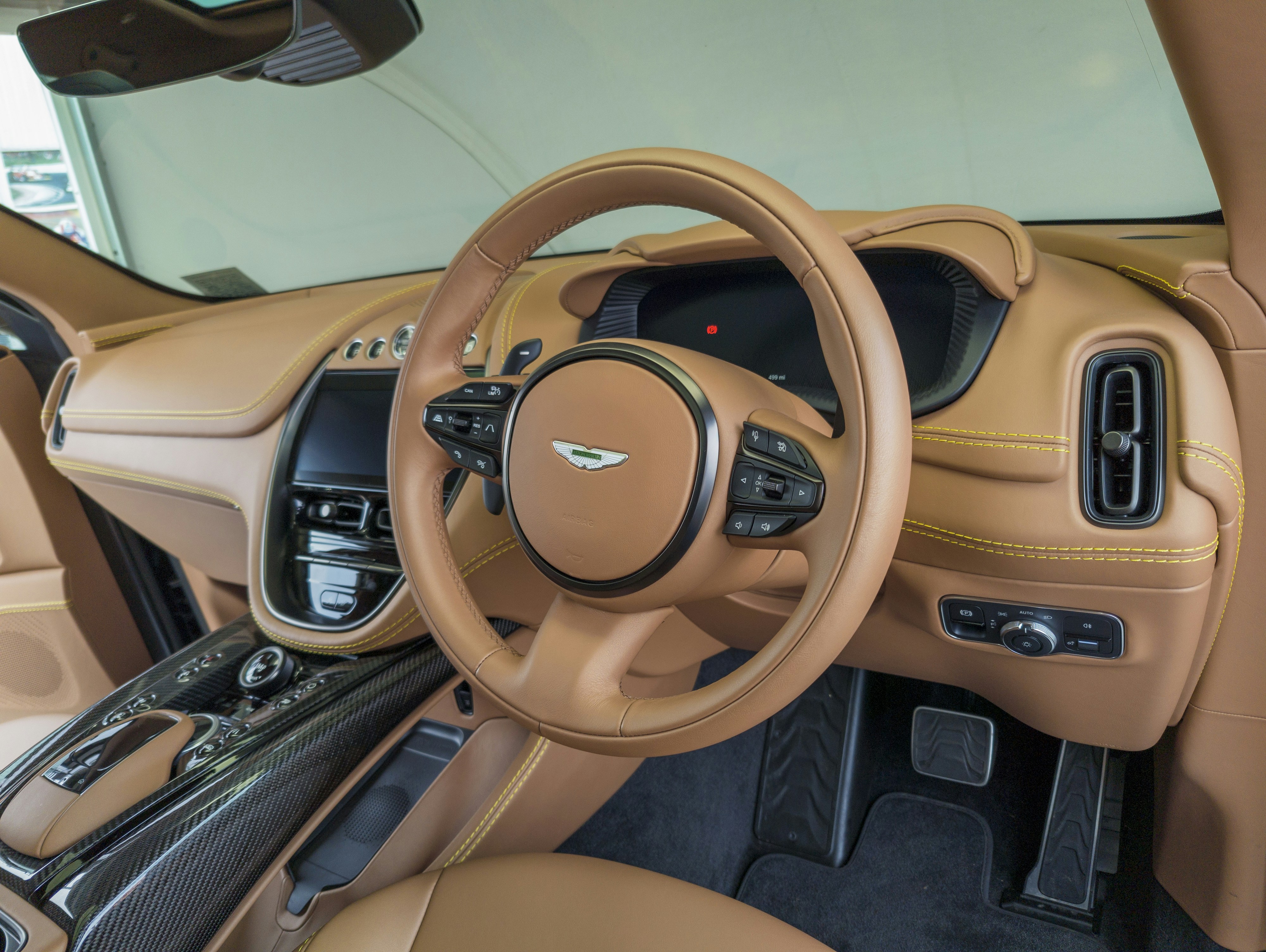 Interior view of a luxury car featuring a plush tan leather steering wheel and dashboard with sleek carbon fiber accents. The design emphasizes sophistication and modern craftsmanship.