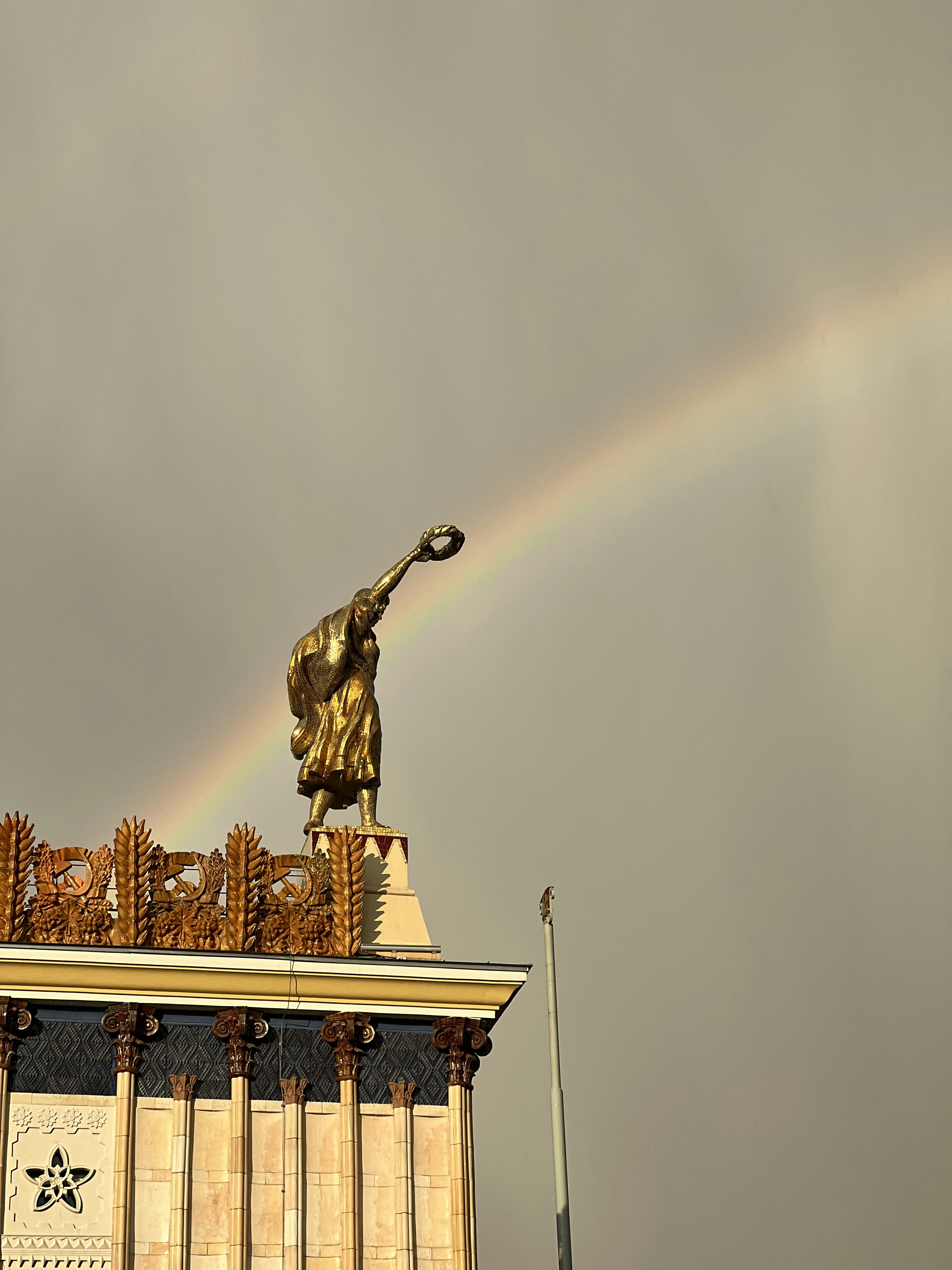 Rainbow Over the Monument: Golden Figure Beside a Vivid Arc