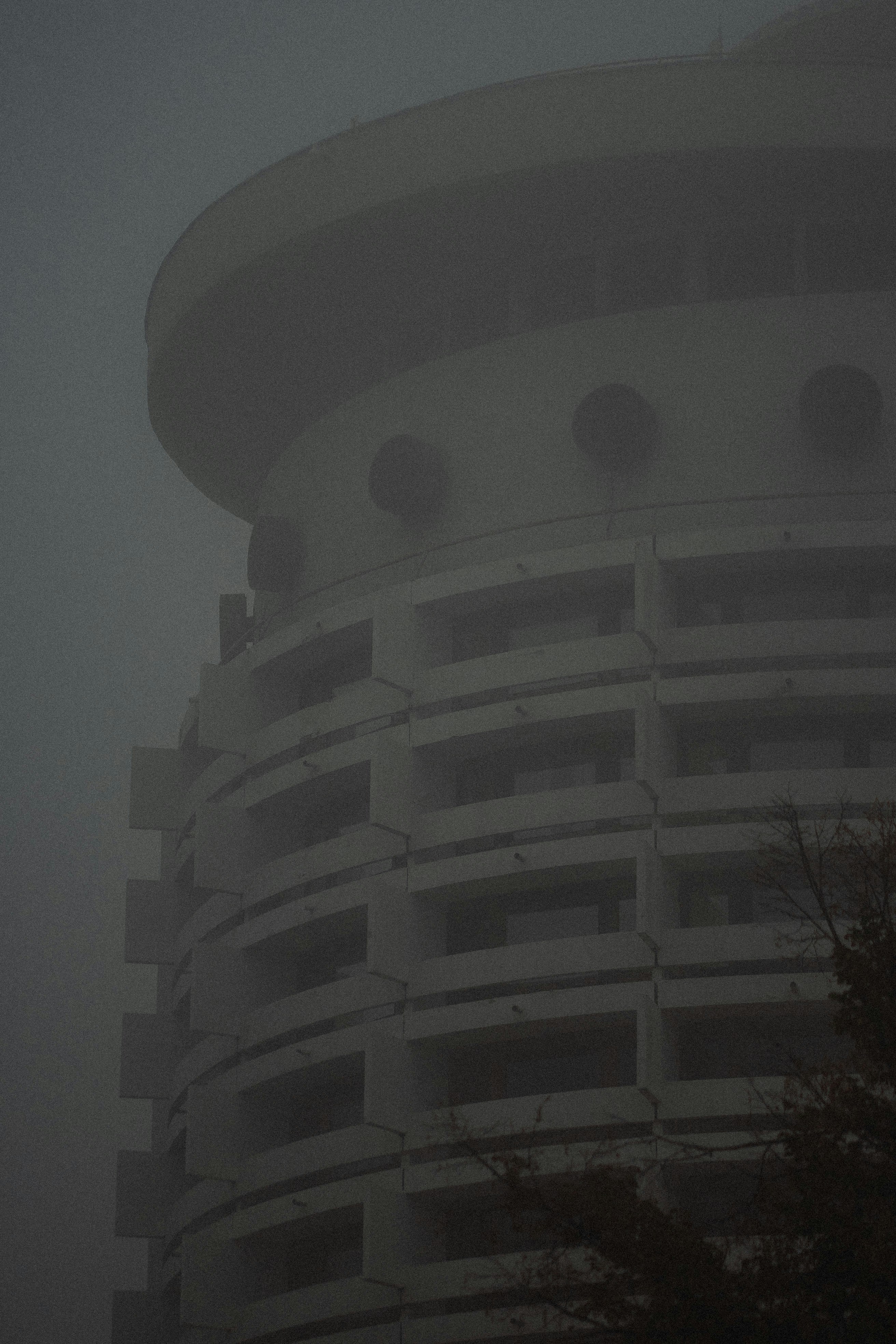 Abstract view of a modern building shrouded in thick fog, highlighting its unique cylindrical structure and layered balconies.