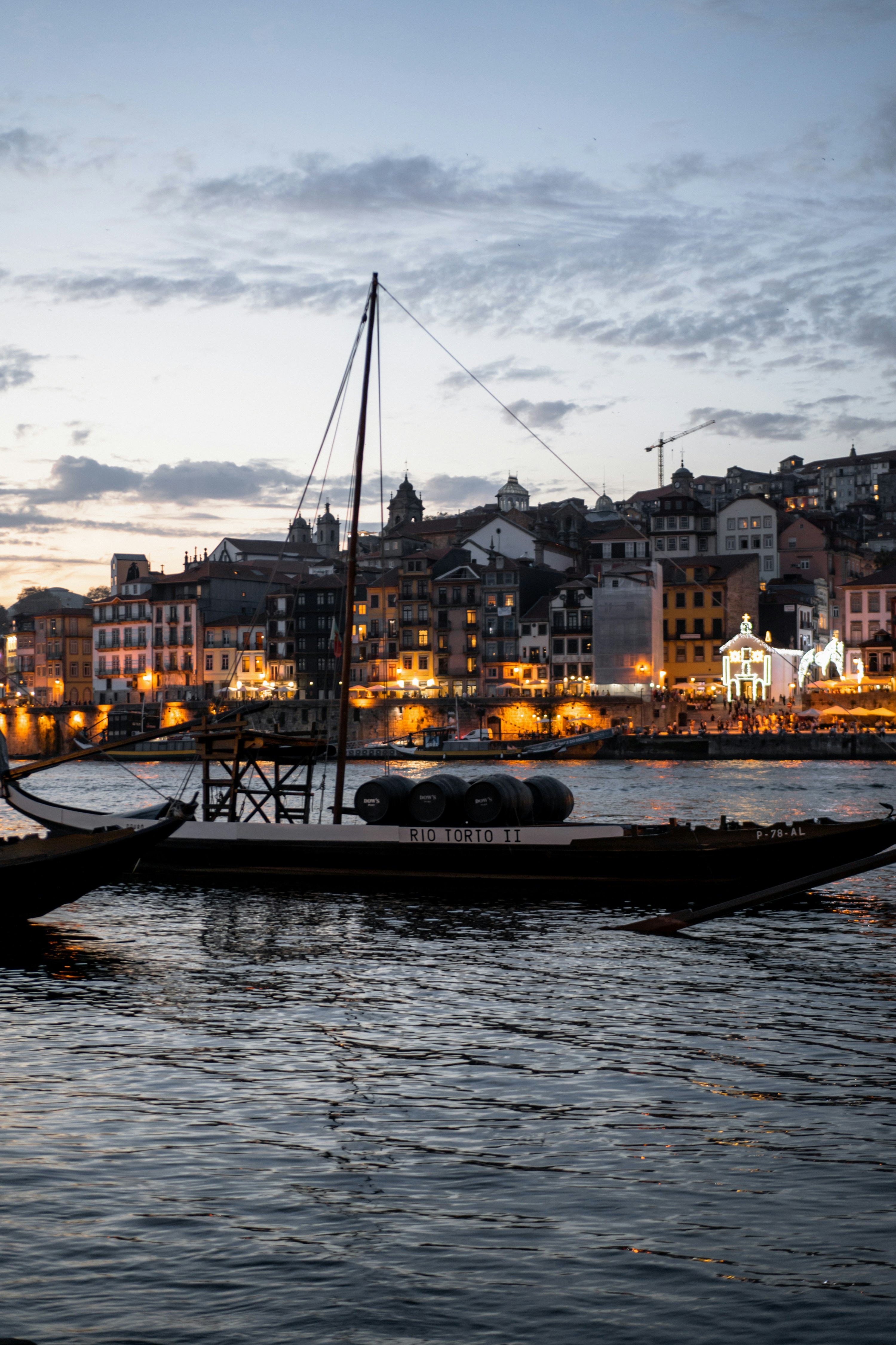 Dusk over a Glow-Lit Harbor: A Sailboat Framed by a Hillside Town