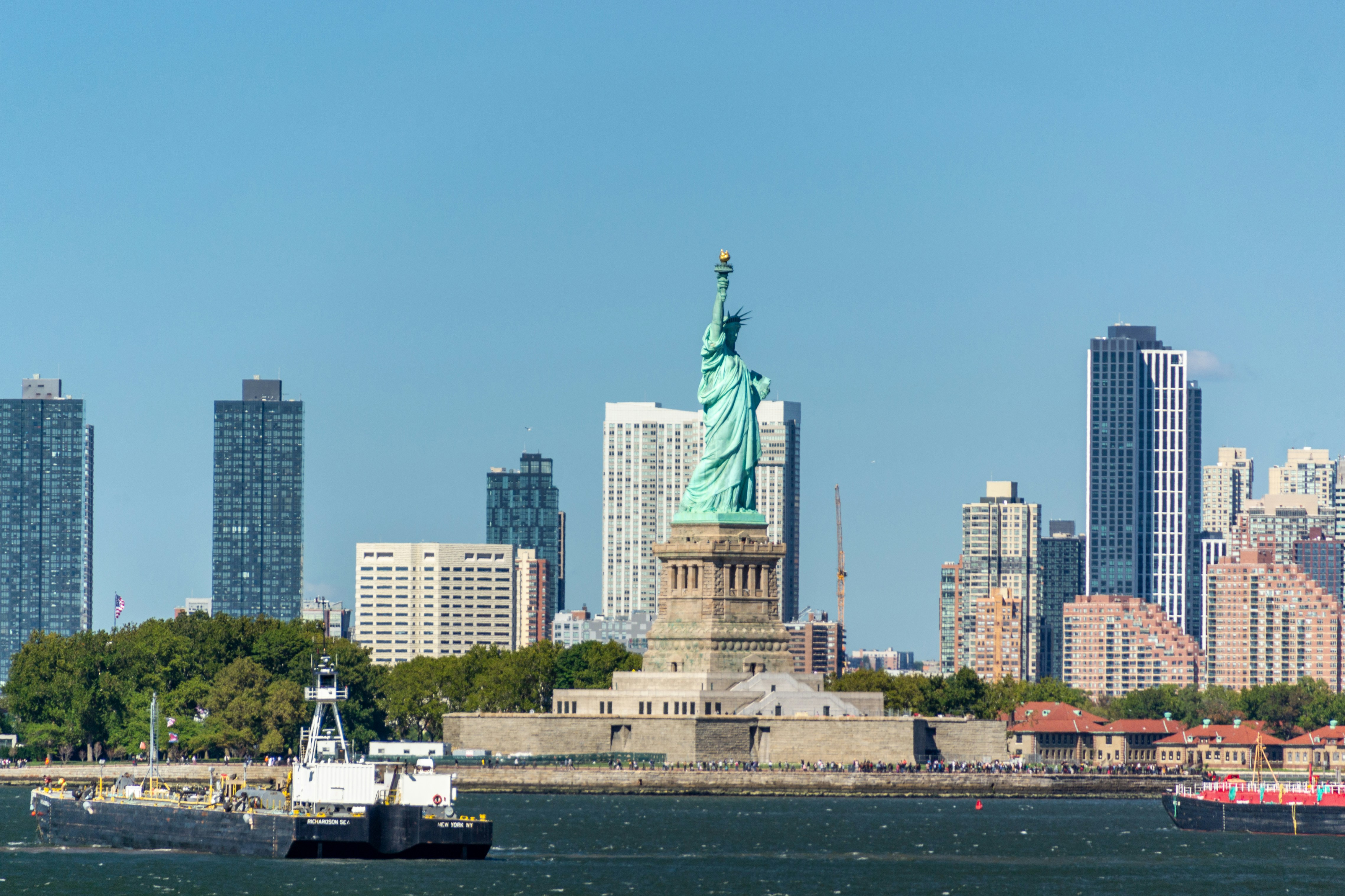 Statue of Liberty standing tall with New York City skyscrapers in the background under a clear blue sky.