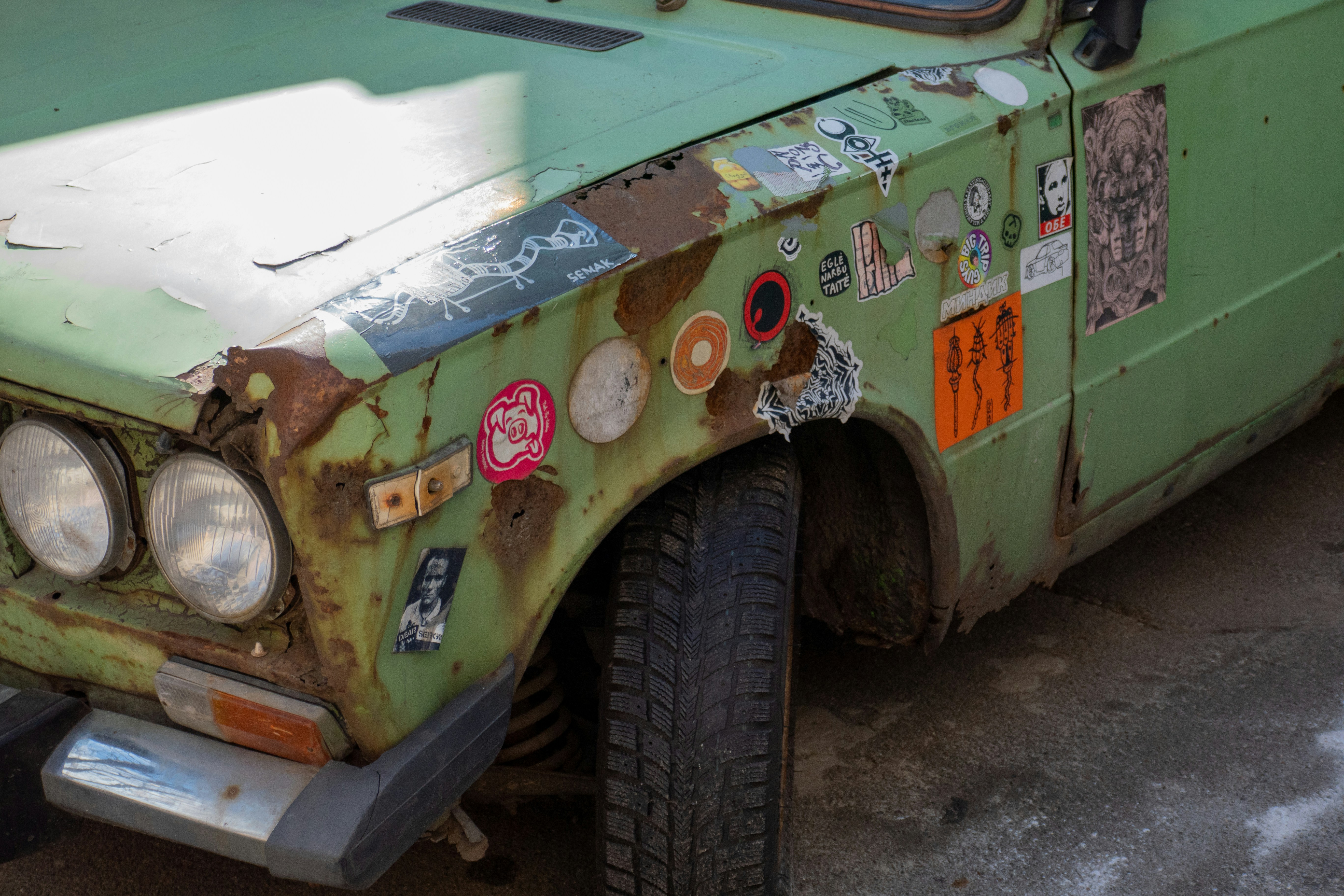 Close-up of a vintage car adorned with various colorful stickers, showcasing its weathered paint and rusted body. The juxtaposition of art and decay highlights the passage of time.