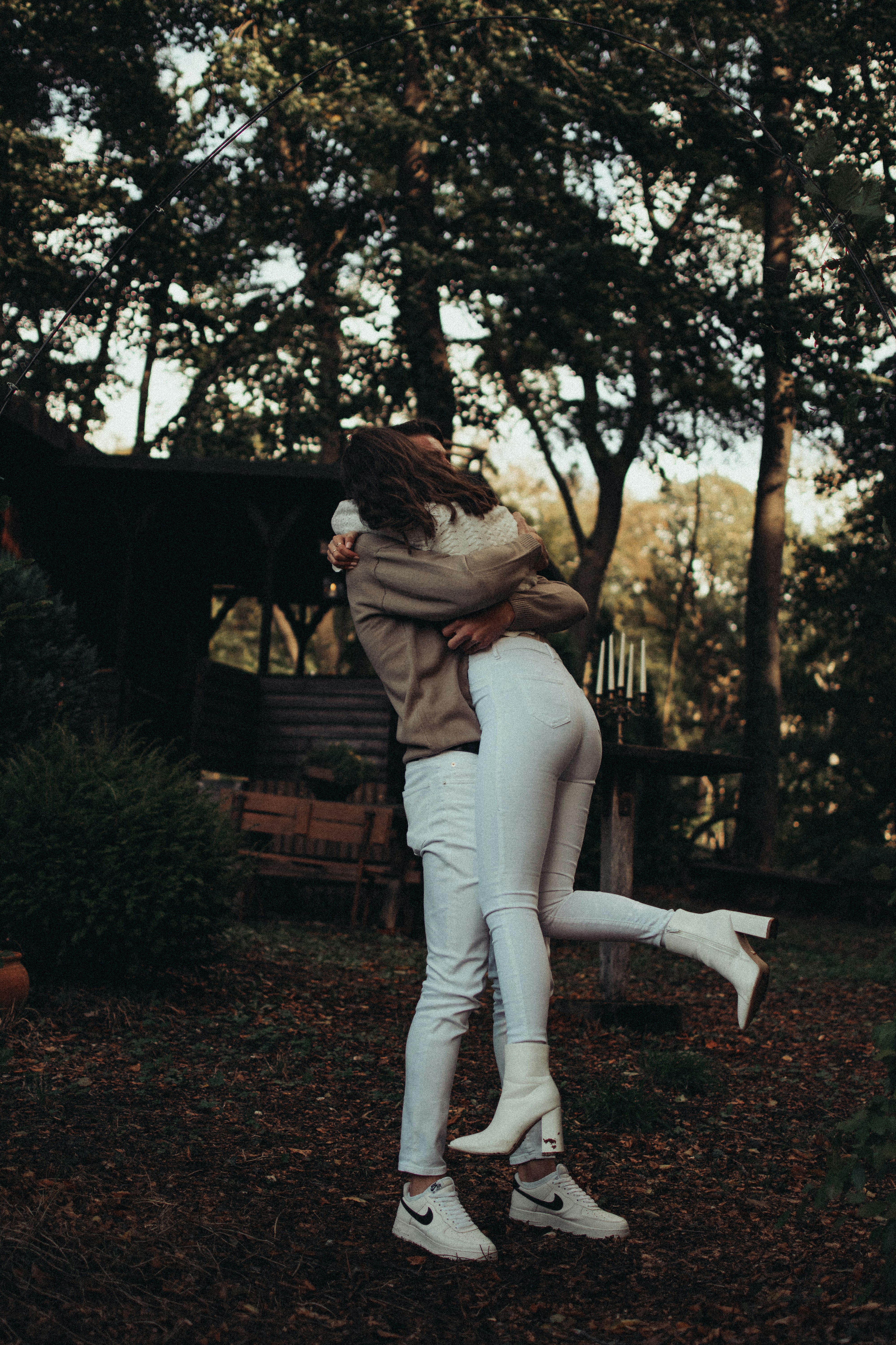 Couple joyfully embracing in a forest setting, surrounded by greenery and rustic elements. The scene captures a moment of intimacy and connection.