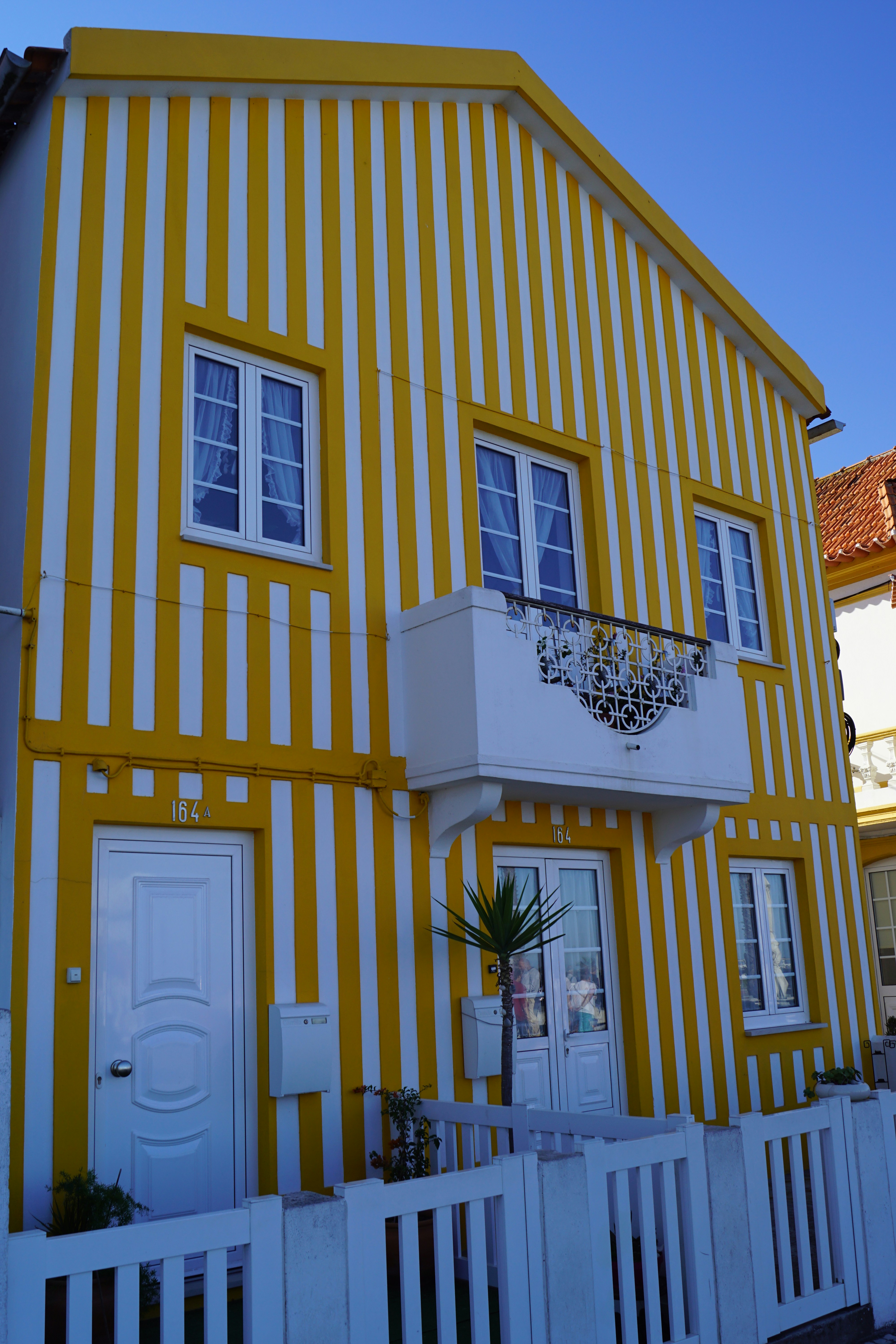 Colorful striped house with white accents and decorative balcony in a coastal setting. The facade showcases a unique architectural style.