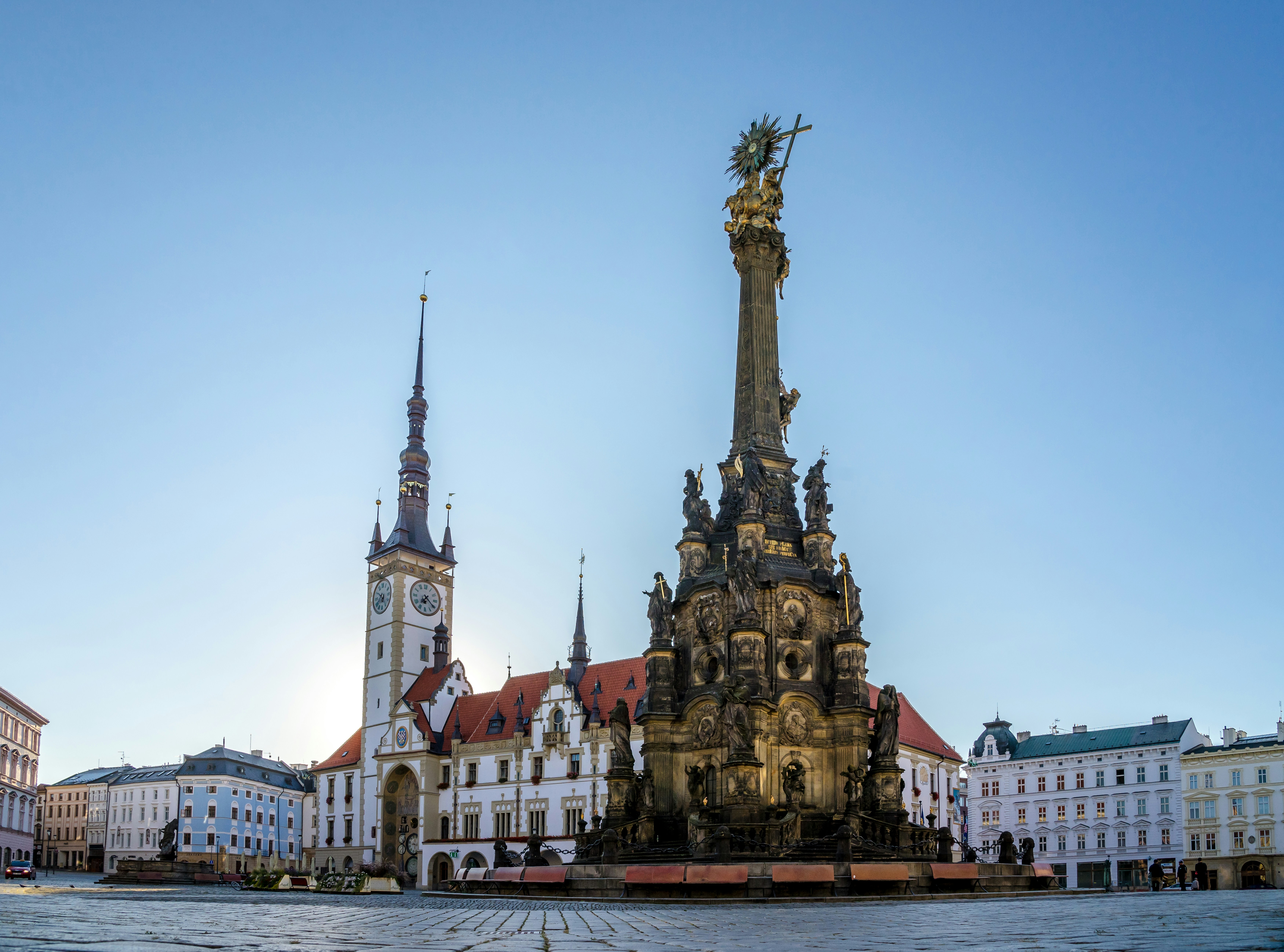 Baroque column and historic church tower set against a clear blue sky in a city square.
