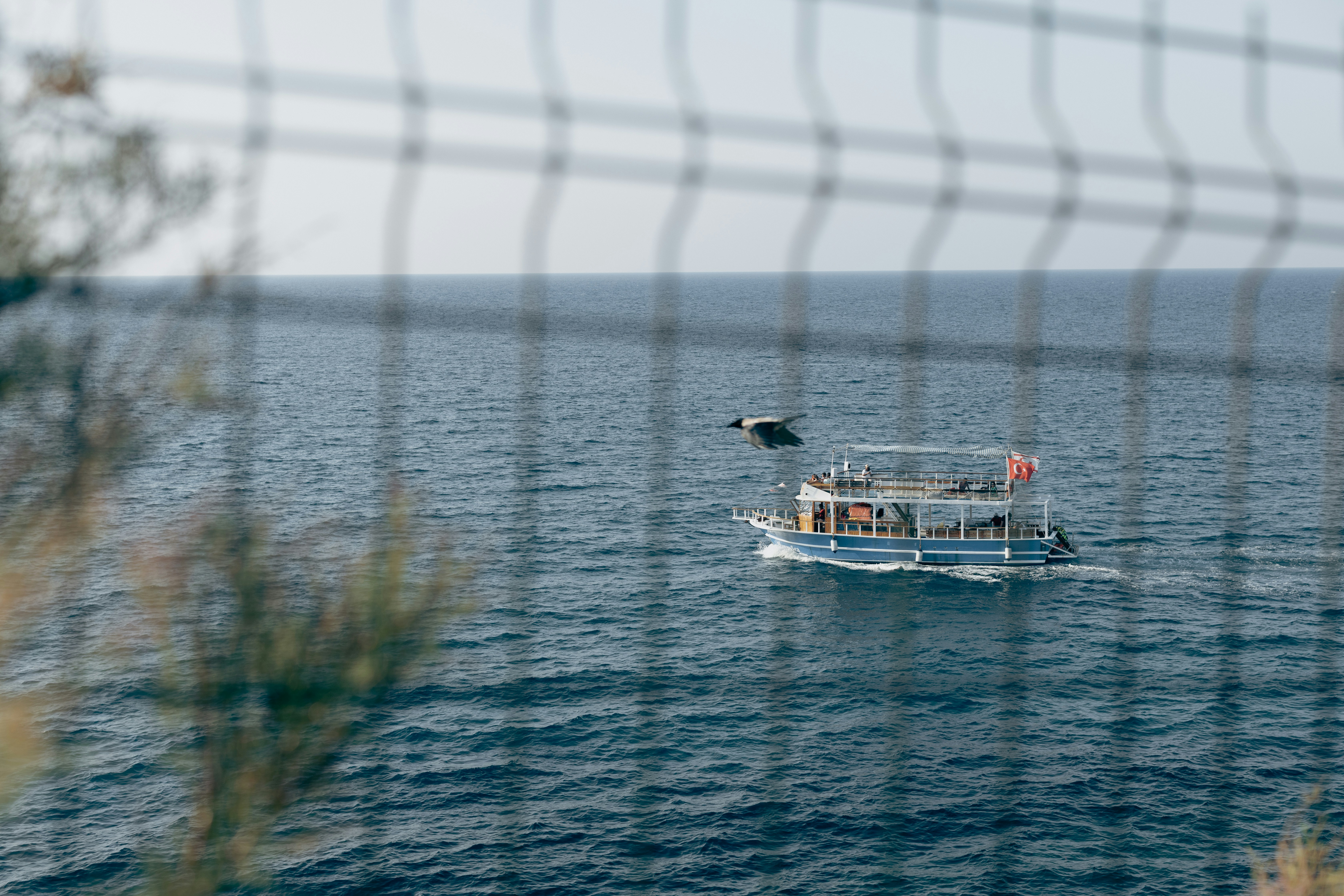 Boat on Calm Turquoise Waters: A Distant Vessel Framed by a Fence-like Foreground