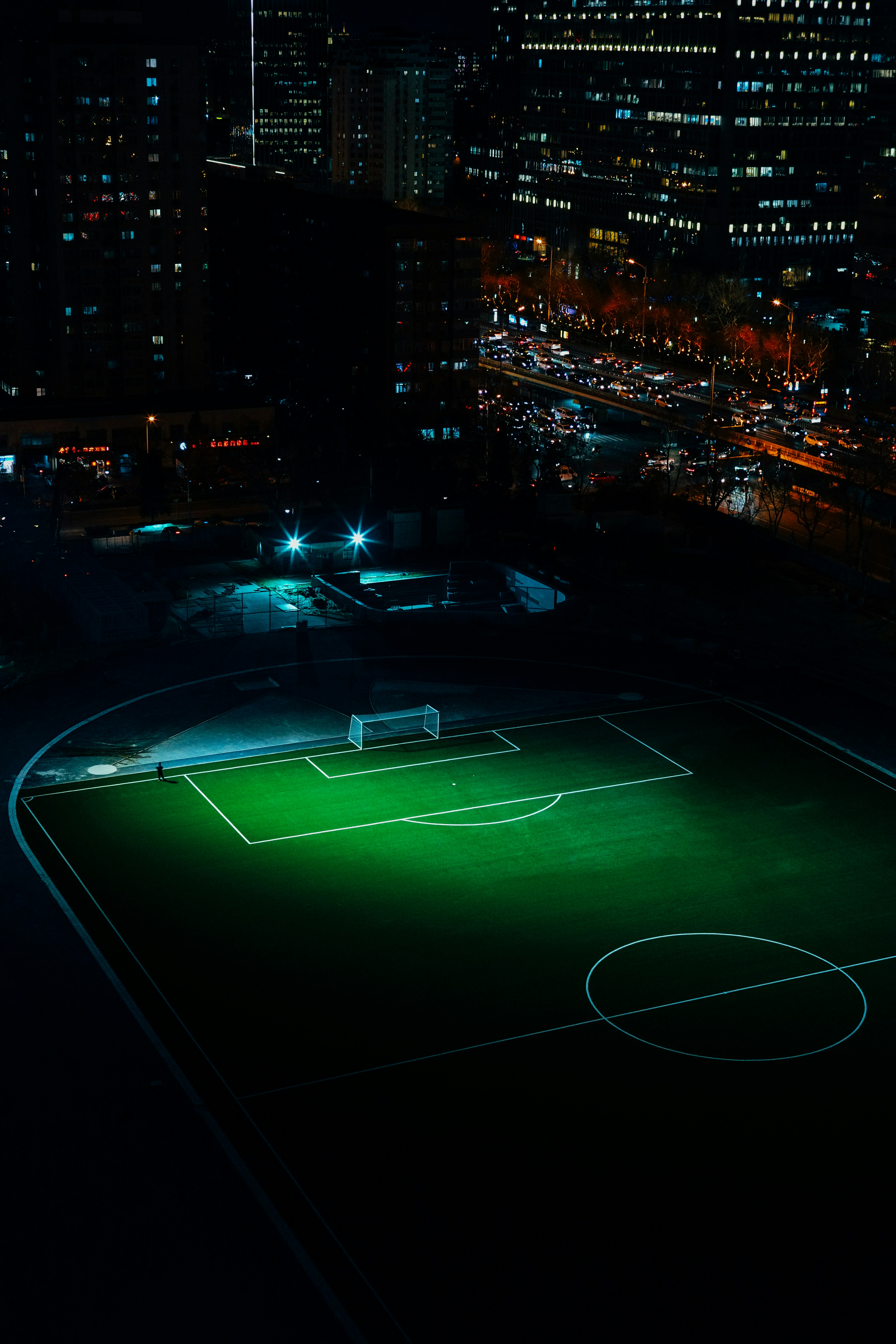 Illuminated soccer field surrounded by city skyscrapers at night, highlighting the contrast between sport and urban life.