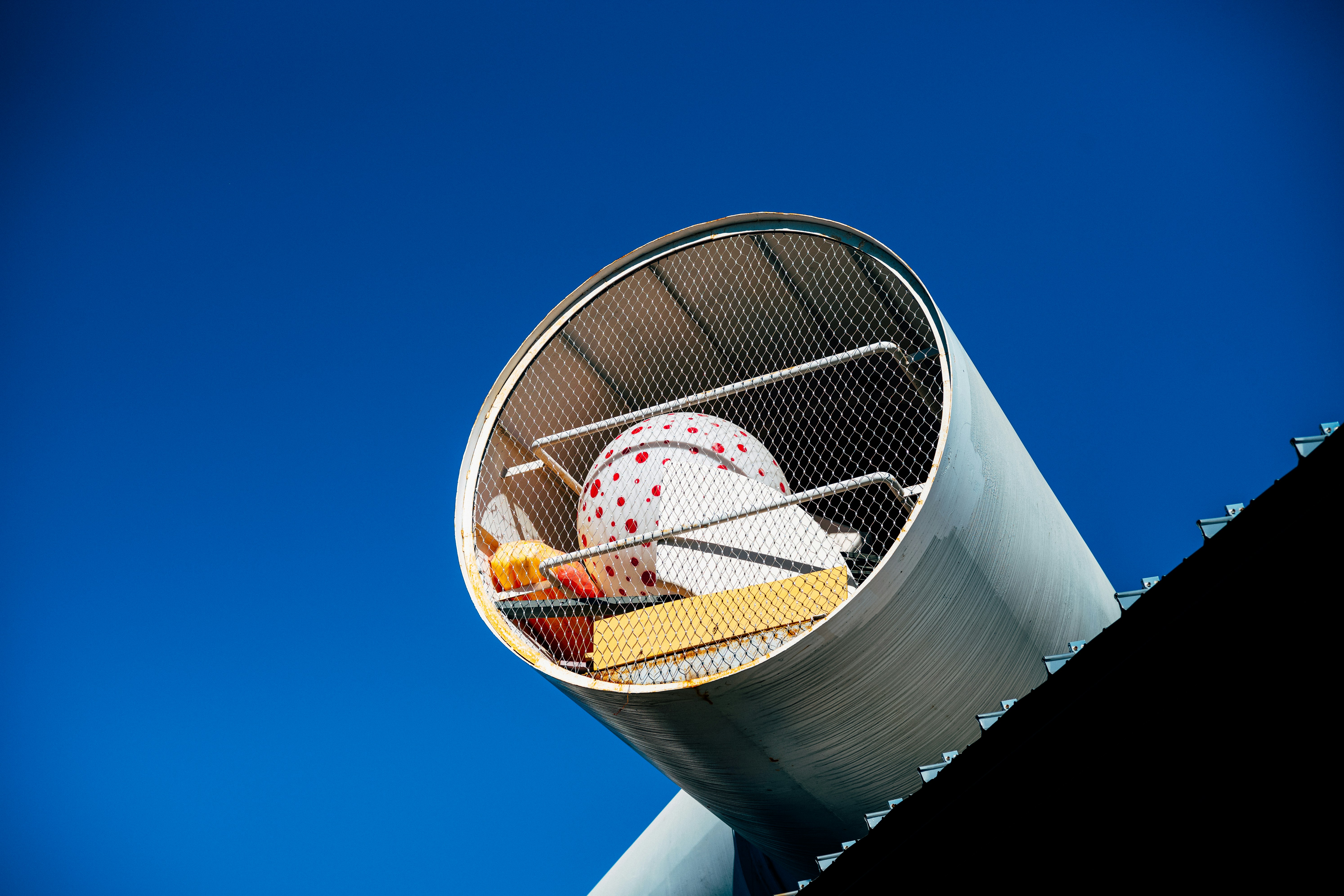 A large, circular ventilation duct against a clear blue sky, featuring a colorful object peeking through its mesh cover.