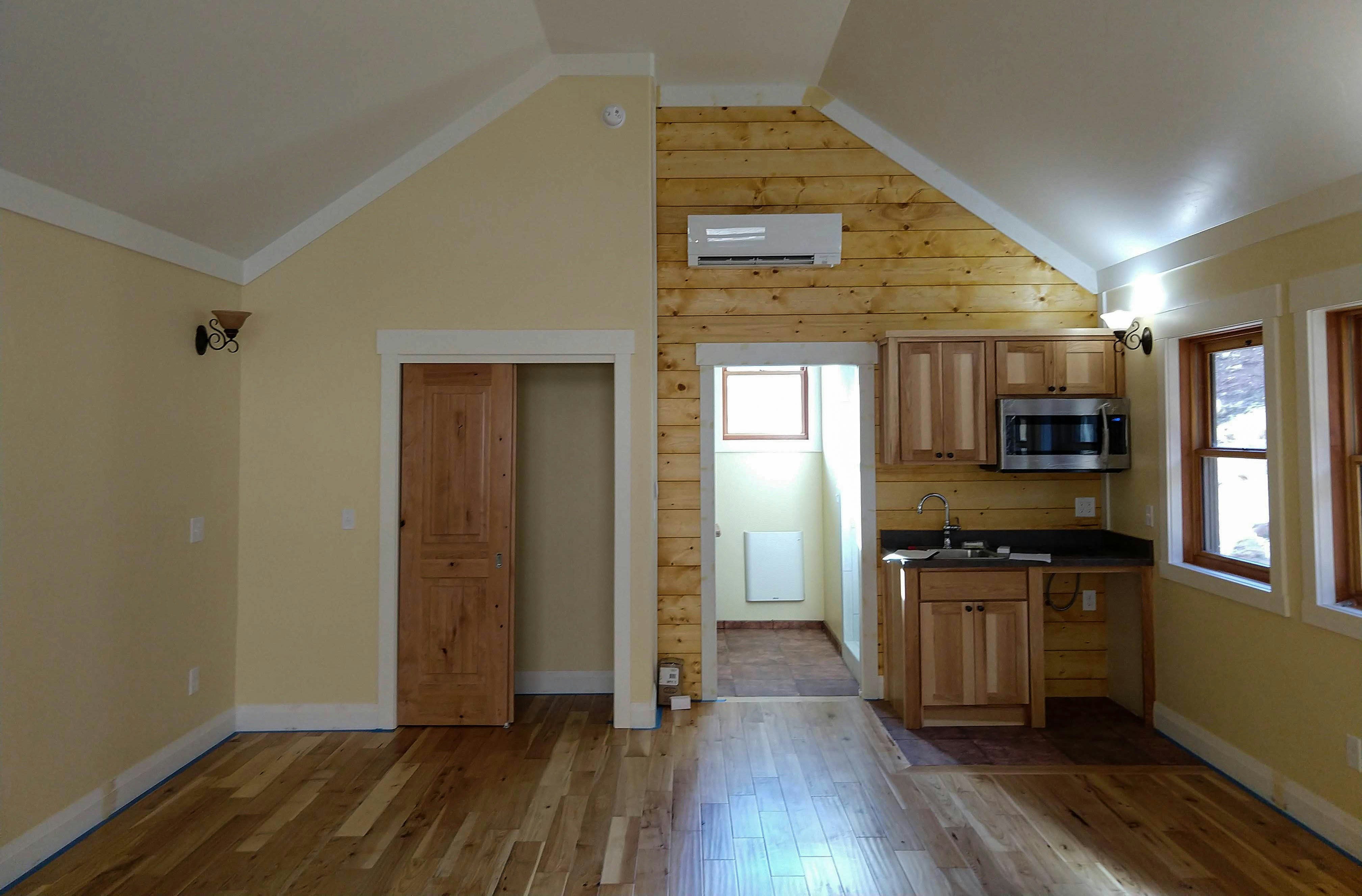 Bright interior of a compact living space featuring wooden accents, a kitchenette, and ample natural light from the windows.
