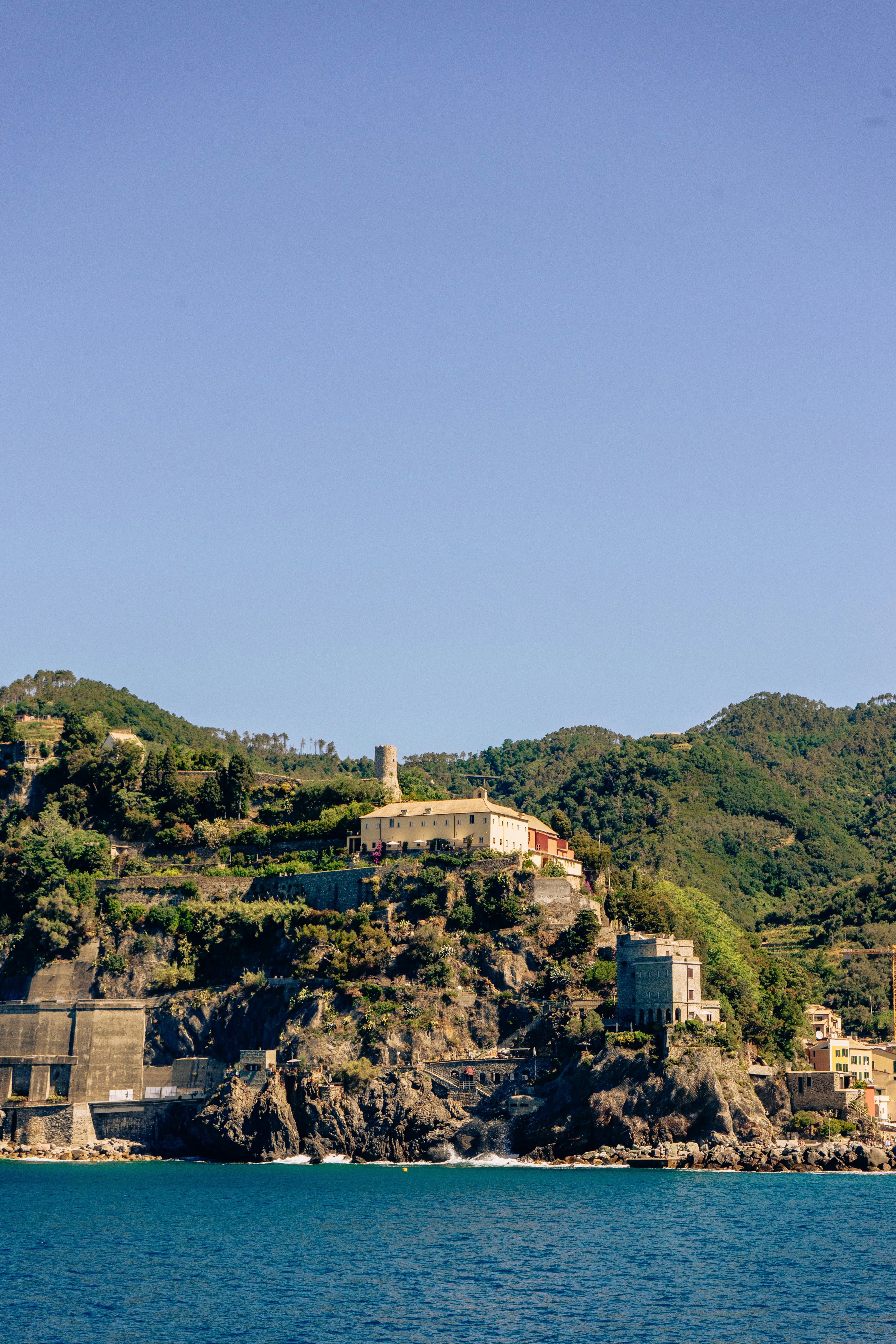 Historic buildings perched on a lush hillside overlooking the tranquil sea, showcasing the harmony between nature and architecture.
