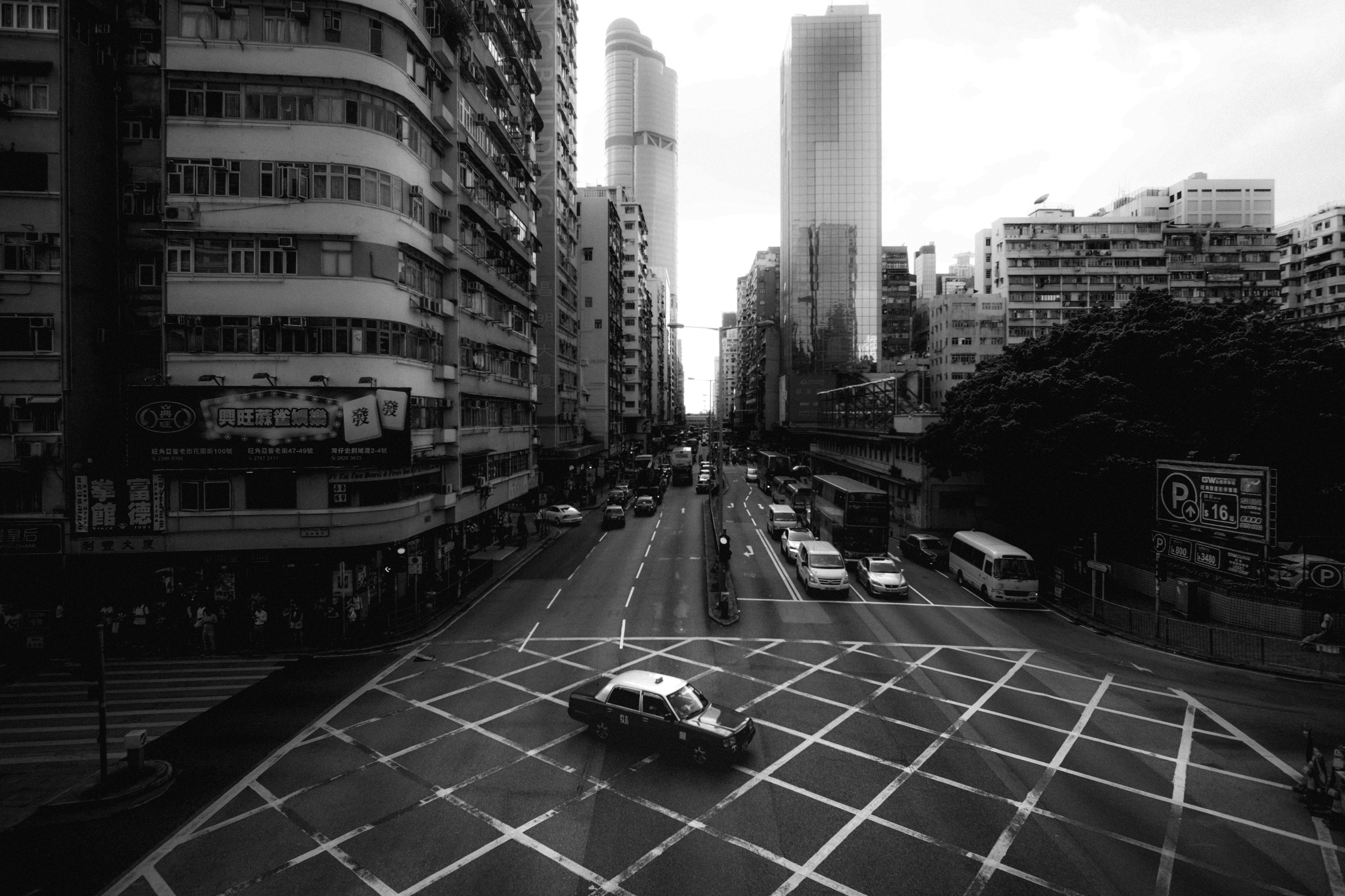 A bustling city intersection captured in black and white, showcasing the contrast between towering skyscrapers and the vibrant street life below.