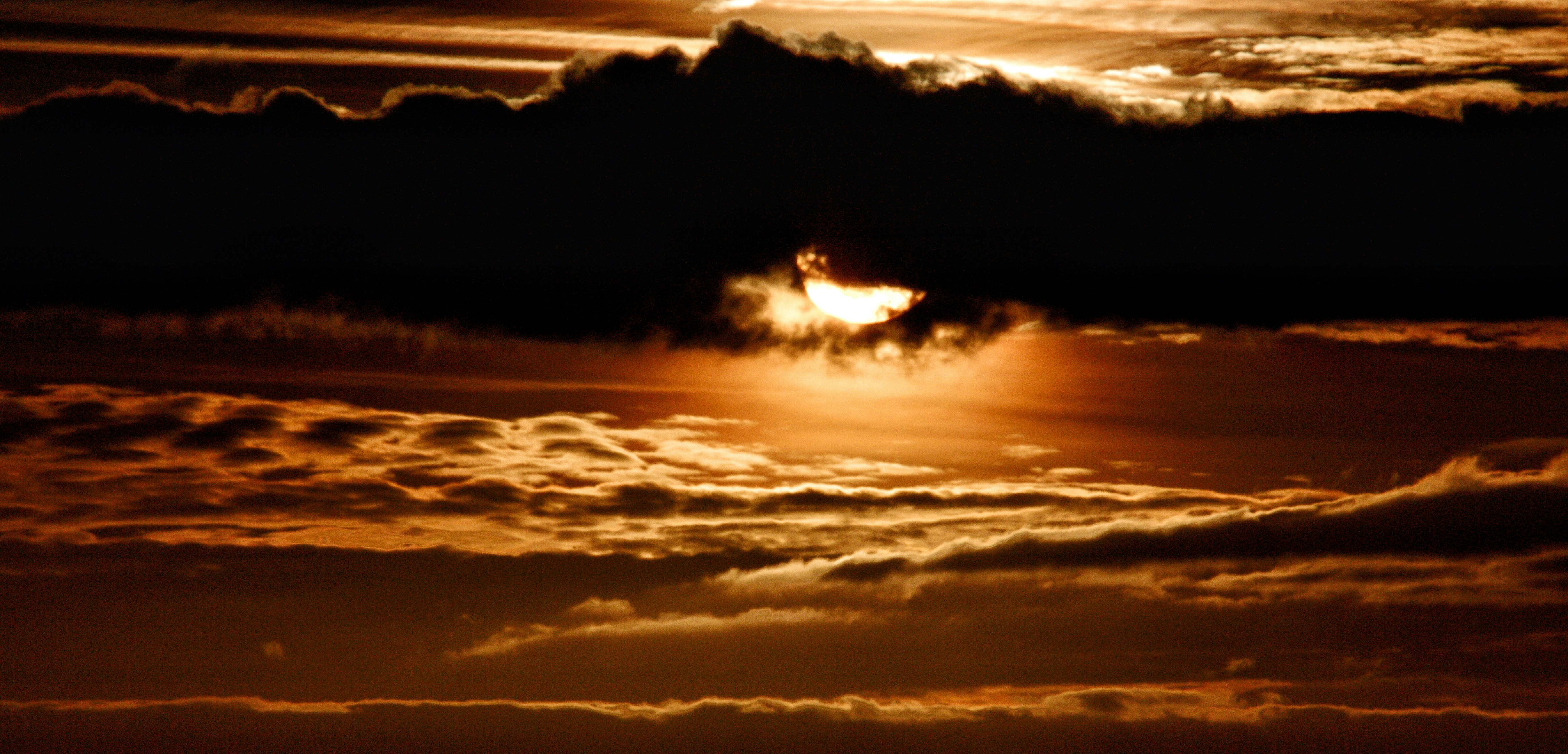 Golden sunlight peeks through dark clouds at dusk, casting a warm glow over the textured sky. The scene captures the transition from day to night.