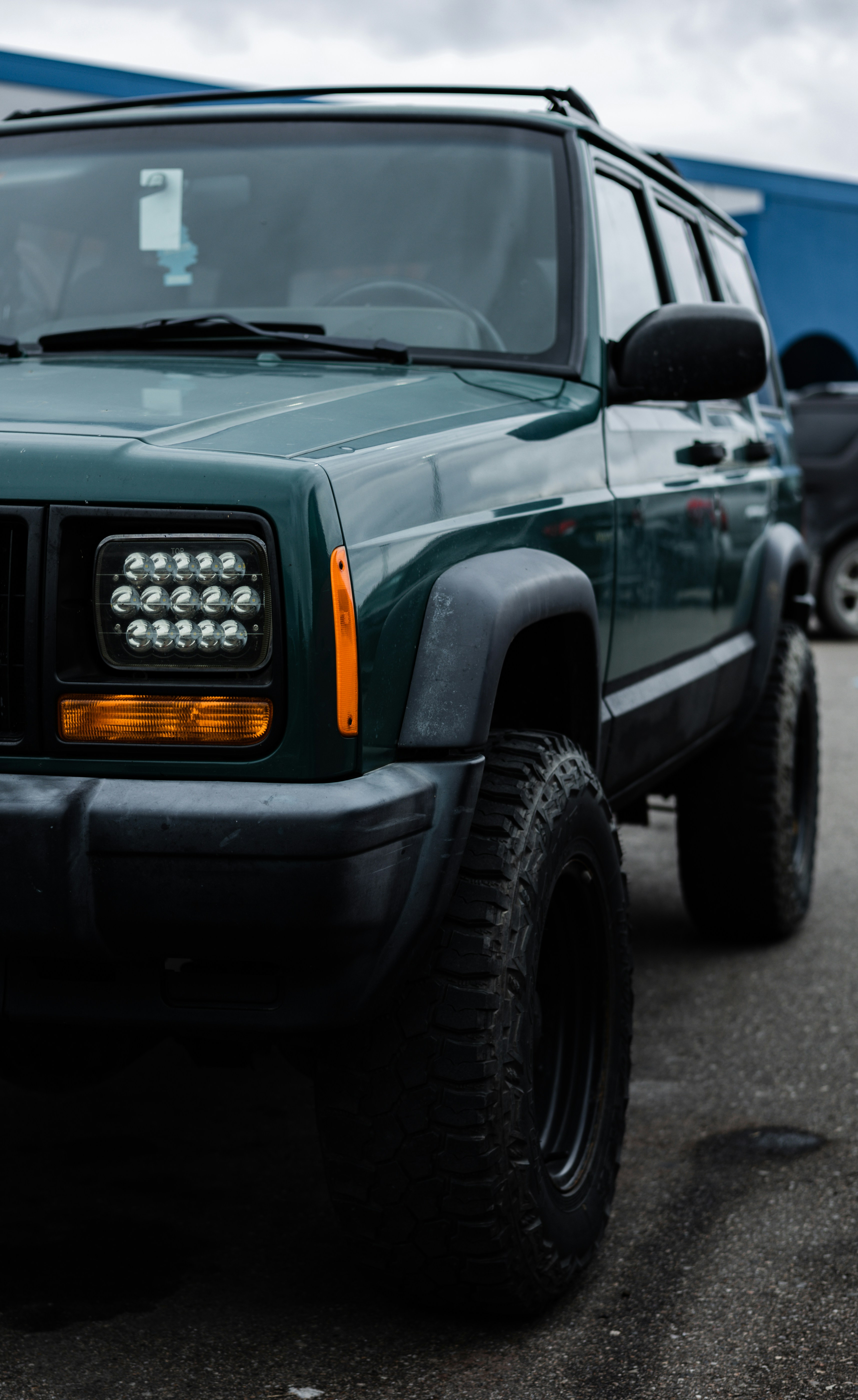 Close-up of a modified green SUV showcasing its aggressive stance and enhanced lighting features. The rugged tires and bold design emphasize its off-road capabilities.