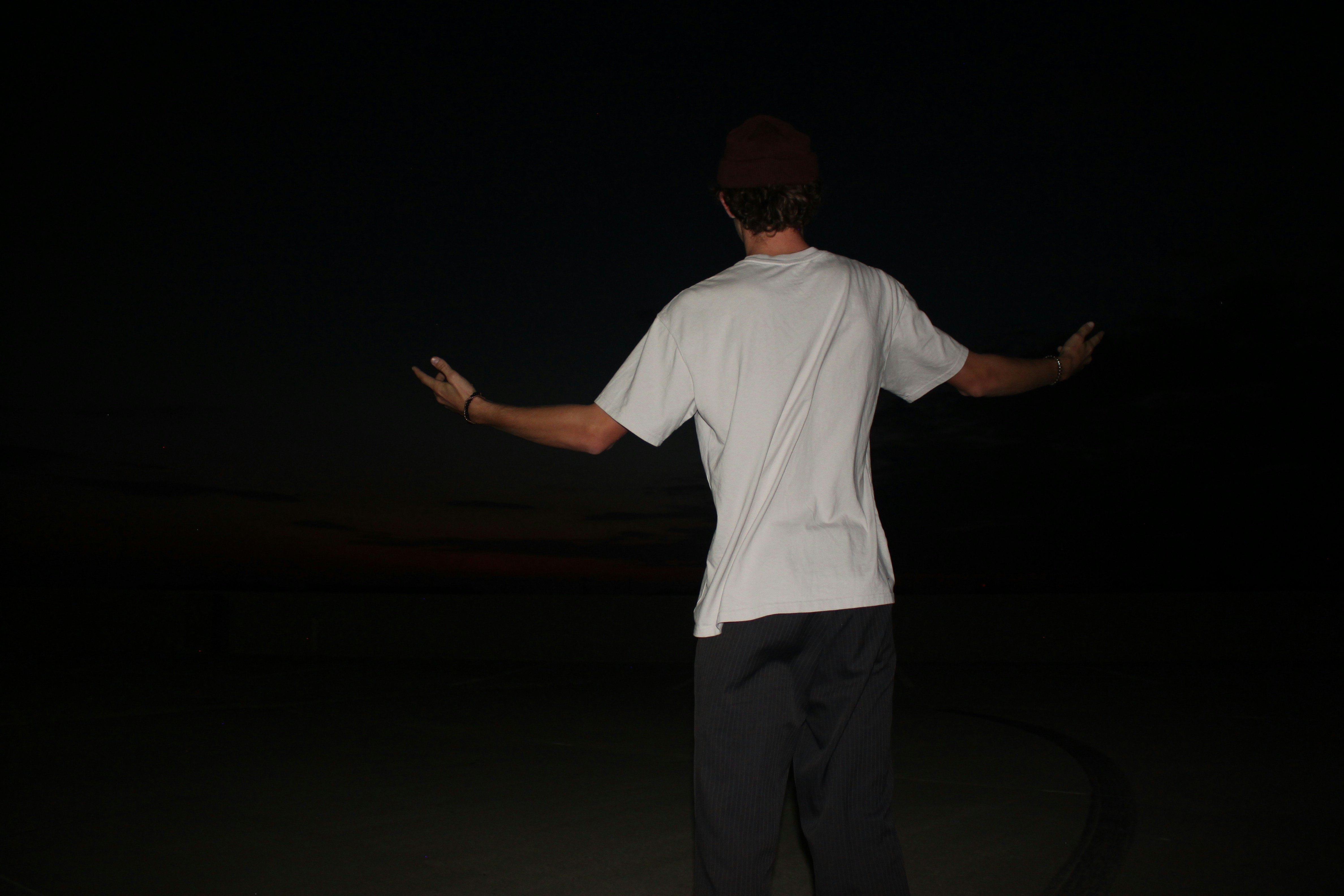 Person in a white shirt facing a dimly lit horizon at dusk.