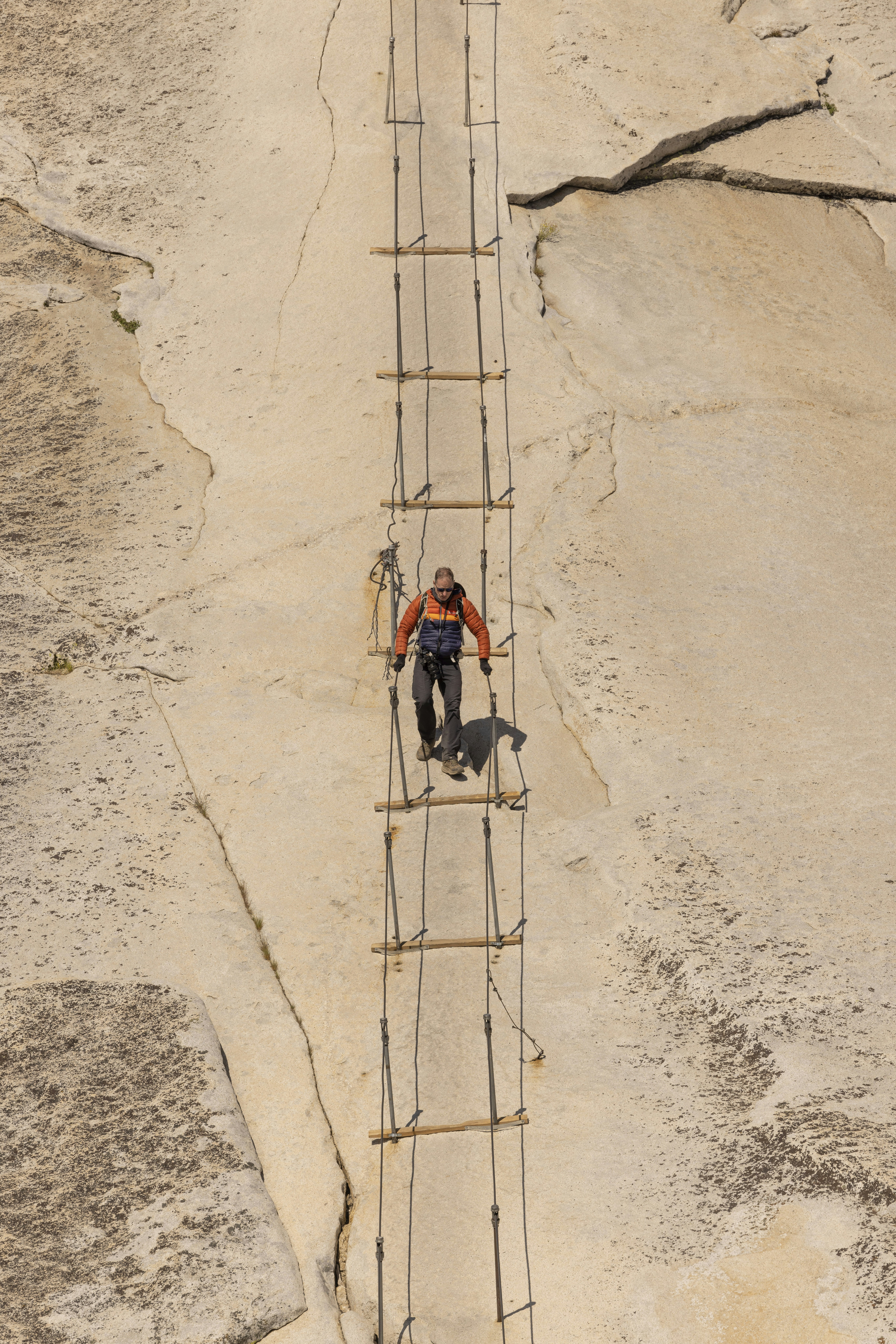 Mid-Climb on a Weathered Rope Ladder Against a Sunlit Cliff
