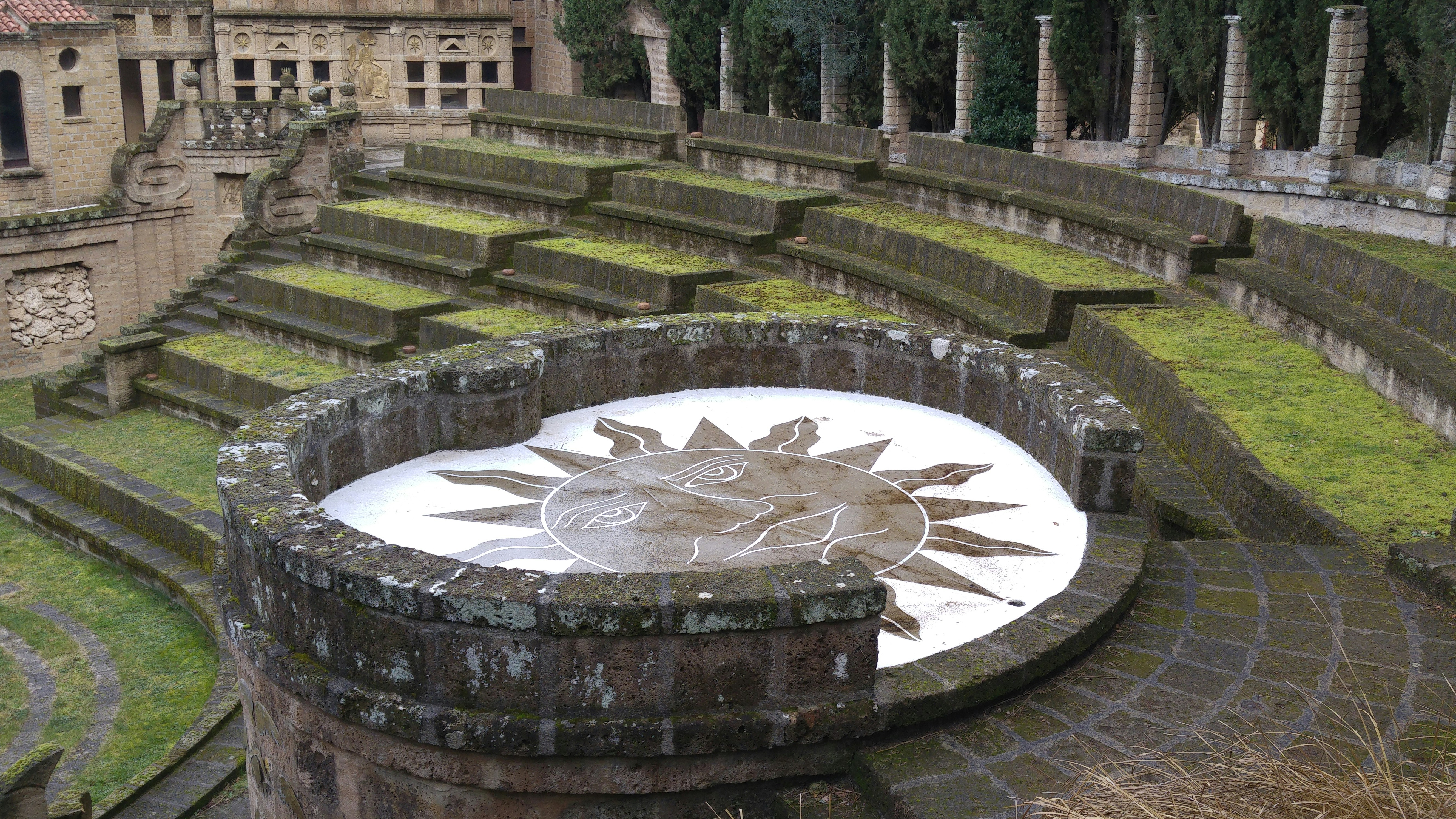 Stone amphitheater with a central sun dial mosaic surrounded by tiered seating and columns.
