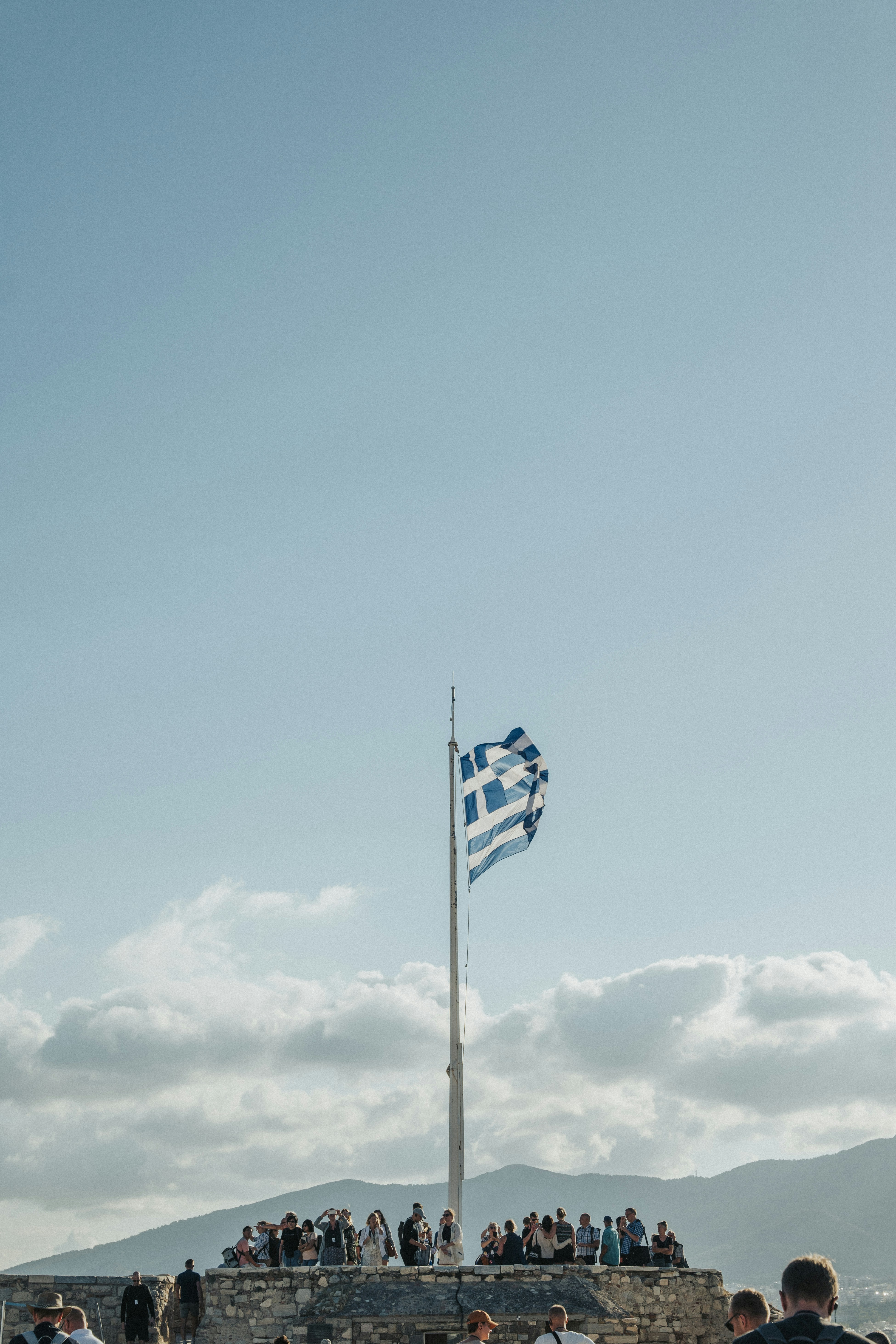 Flag on the Ridge: Aegean Crest Above a Crowded Terrace