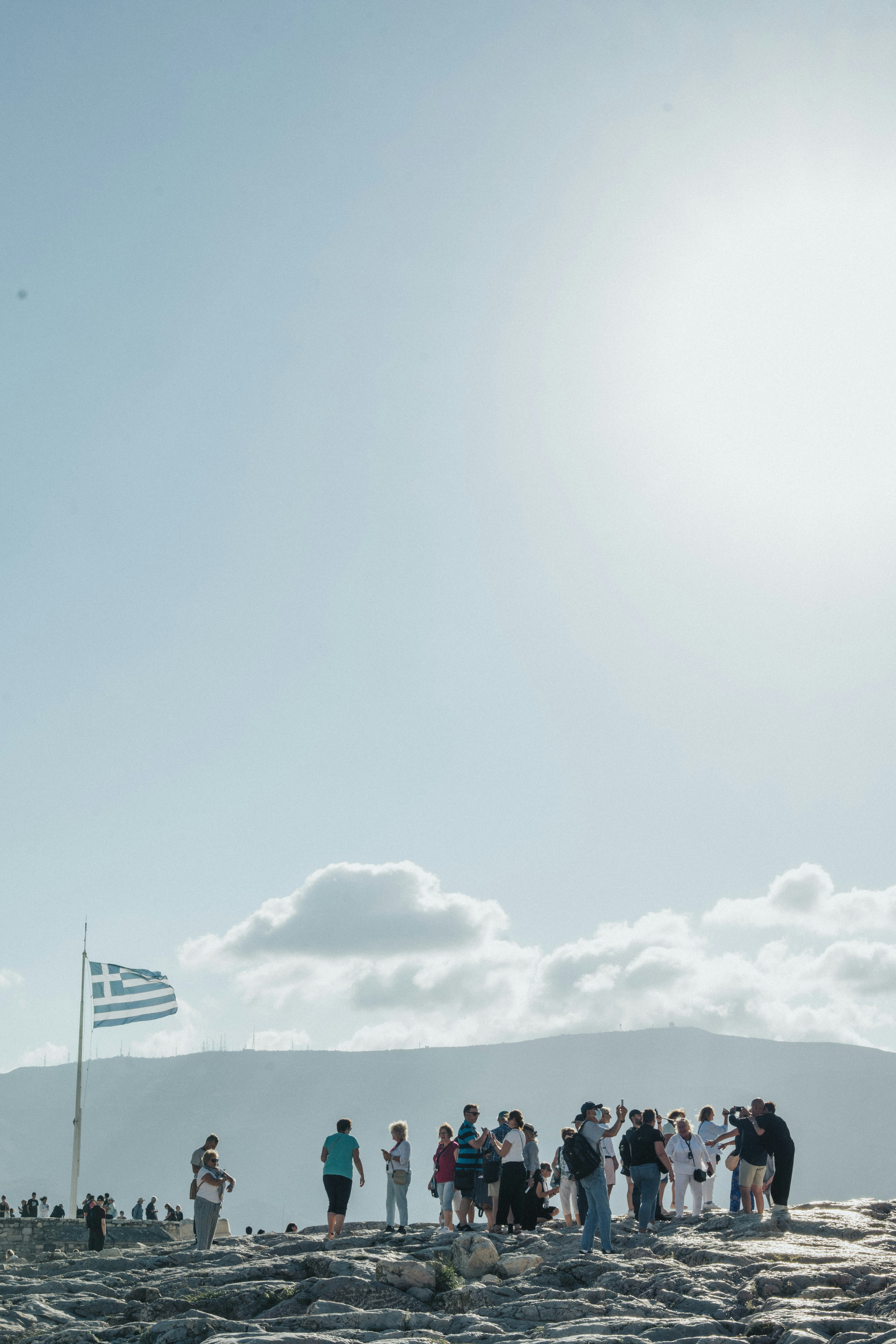 Aegean Cliffside Rendezvous: Crowds Gather Beneath a Waving Greek Flag