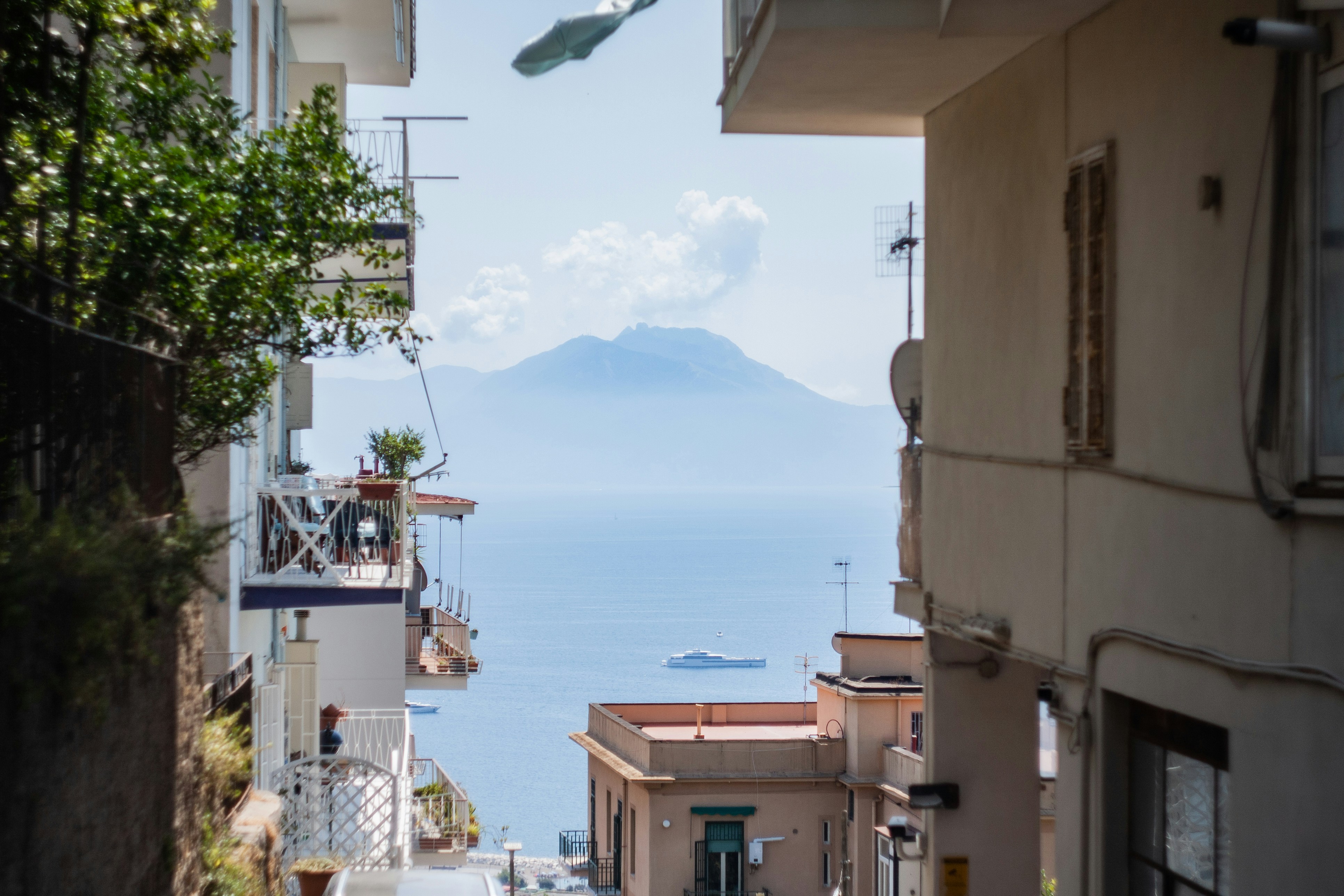 Narrow street framed by buildings with a distant volcano rising above the sea in the background.
