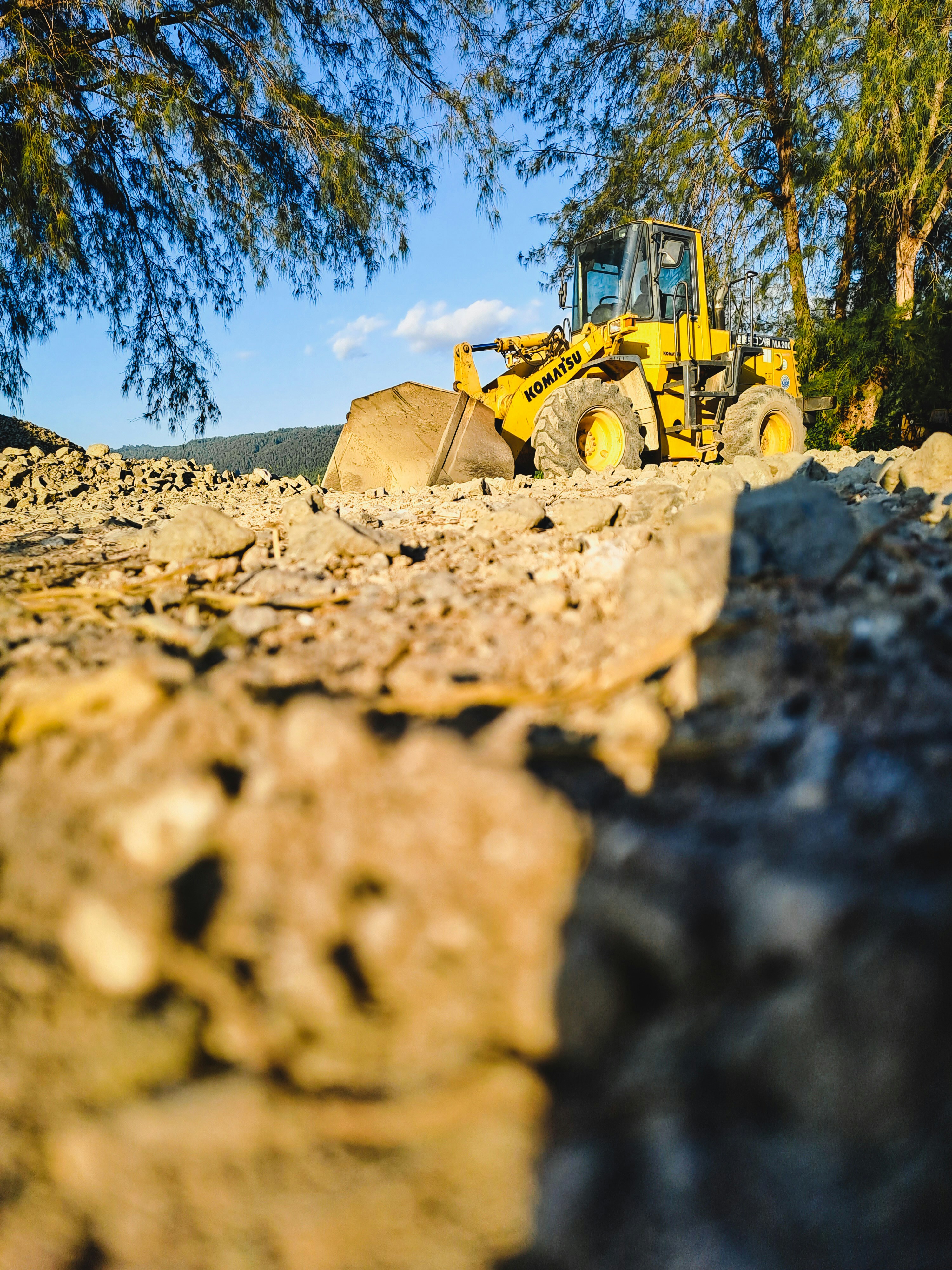 A yellow Komatsu loader maneuvering over rocky terrain under a clear blue sky.