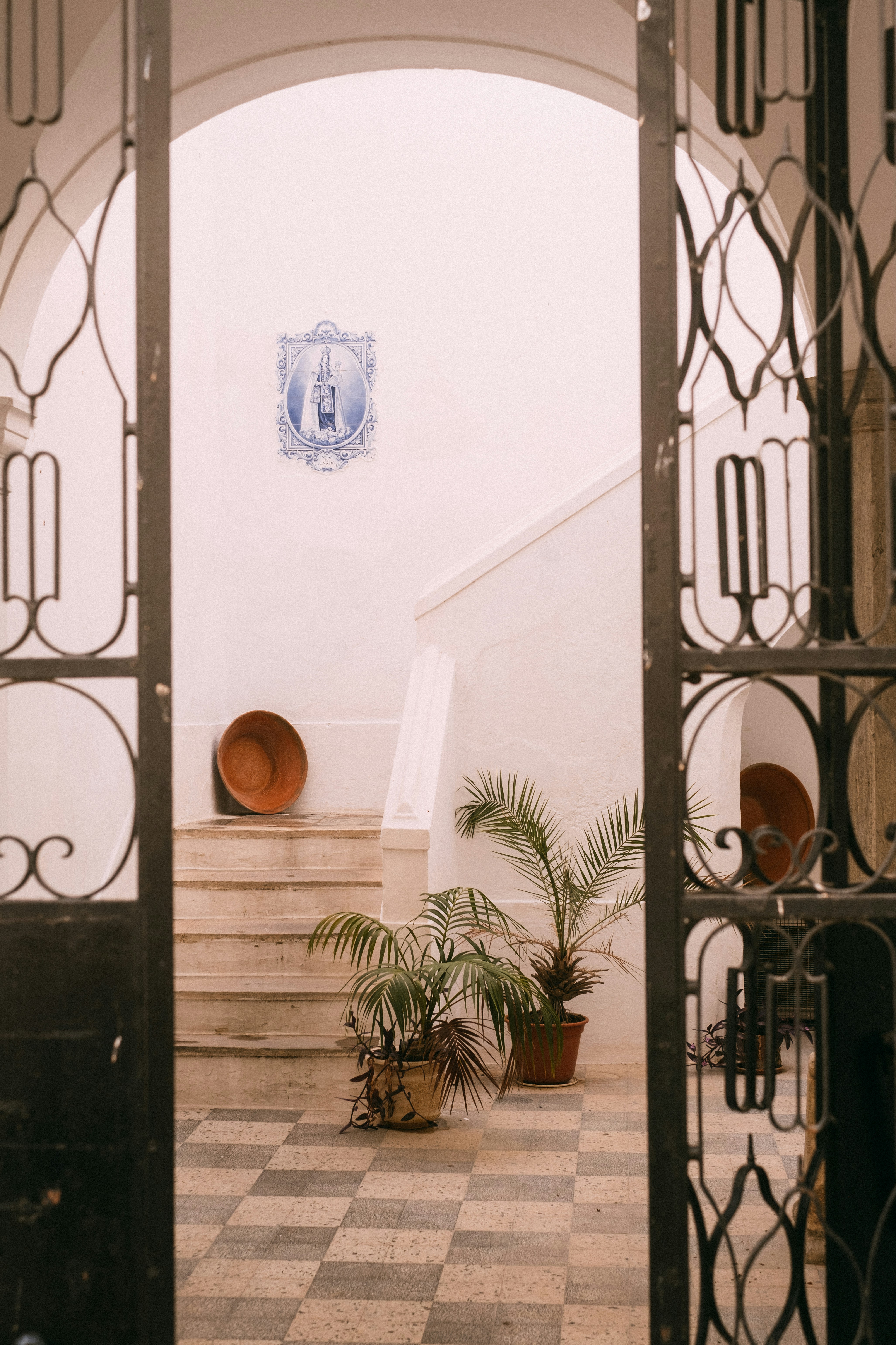 Elegant staircase framed by ornate ironwork, featuring potted plants and decorative pottery. A blue artwork graces the wall, enhancing the peaceful ambiance.
