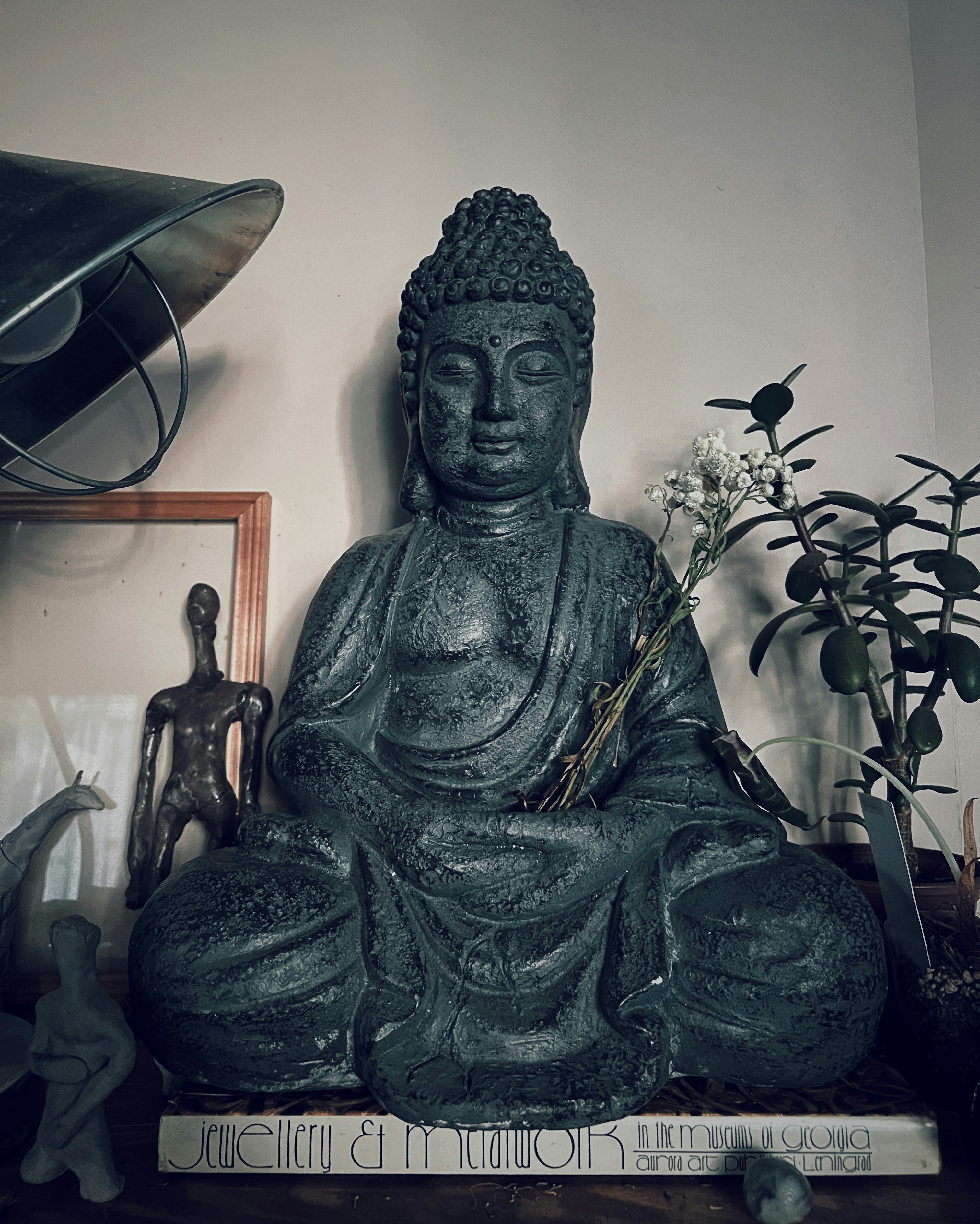 Patina Buddha on a Quiet Shelf Shrine Surrounded by Greenery and Soft Light