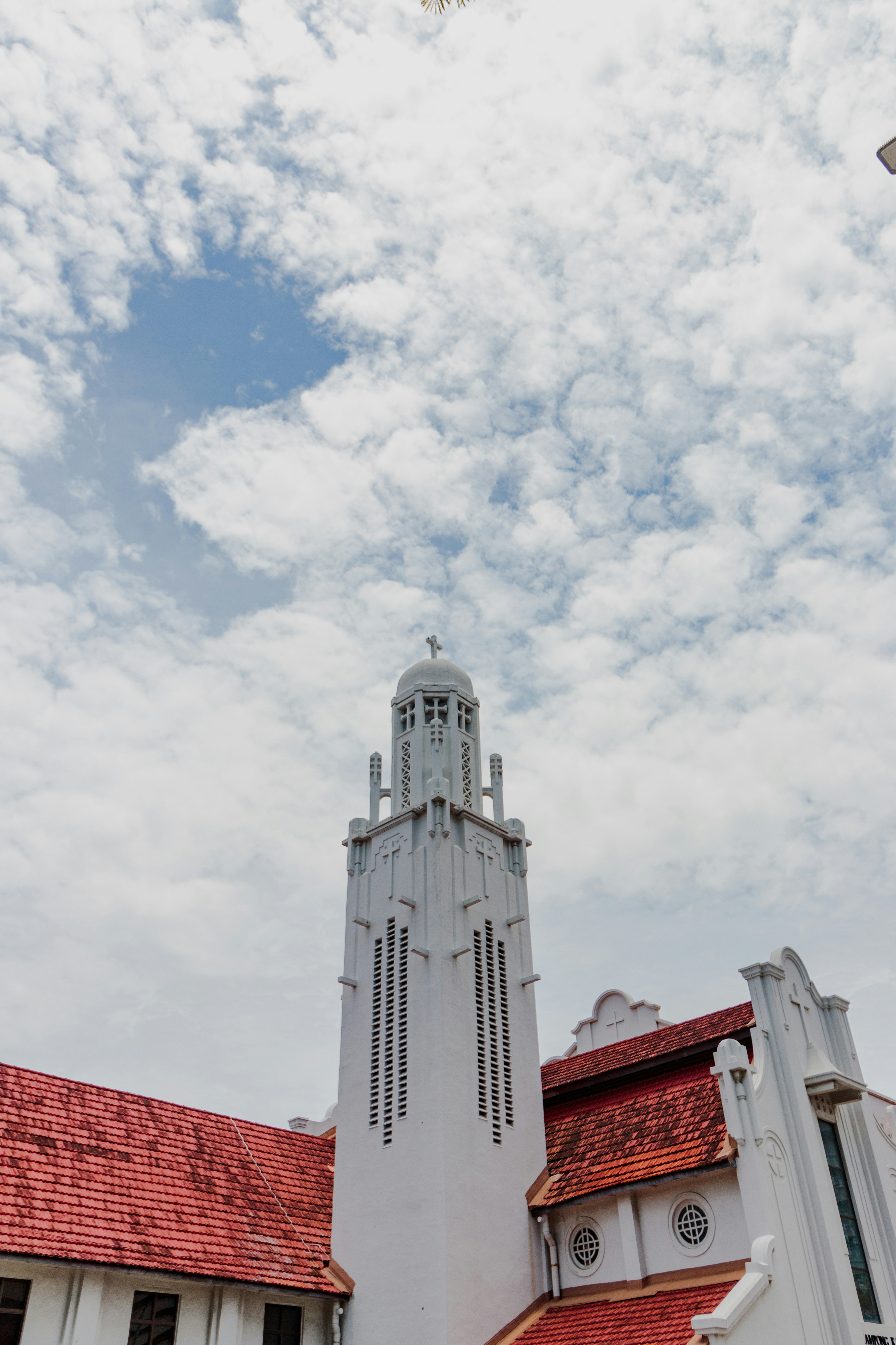 Spire of Serenity: White Tower Rising Over a Red-Tiled Roof Beneath a Quilt of Clouds