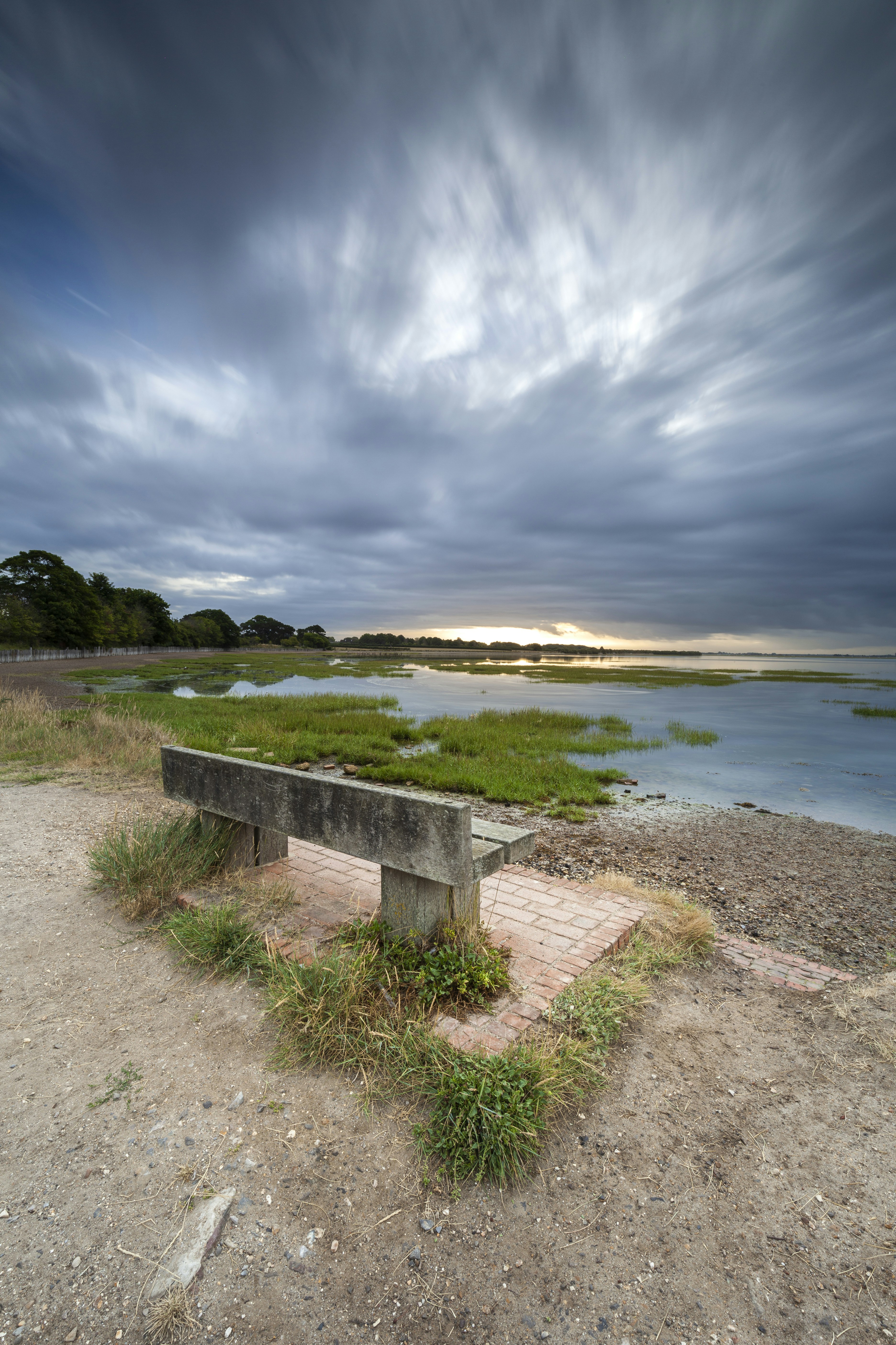 Bench by the shoreline under a sweeping, storm-swept sky