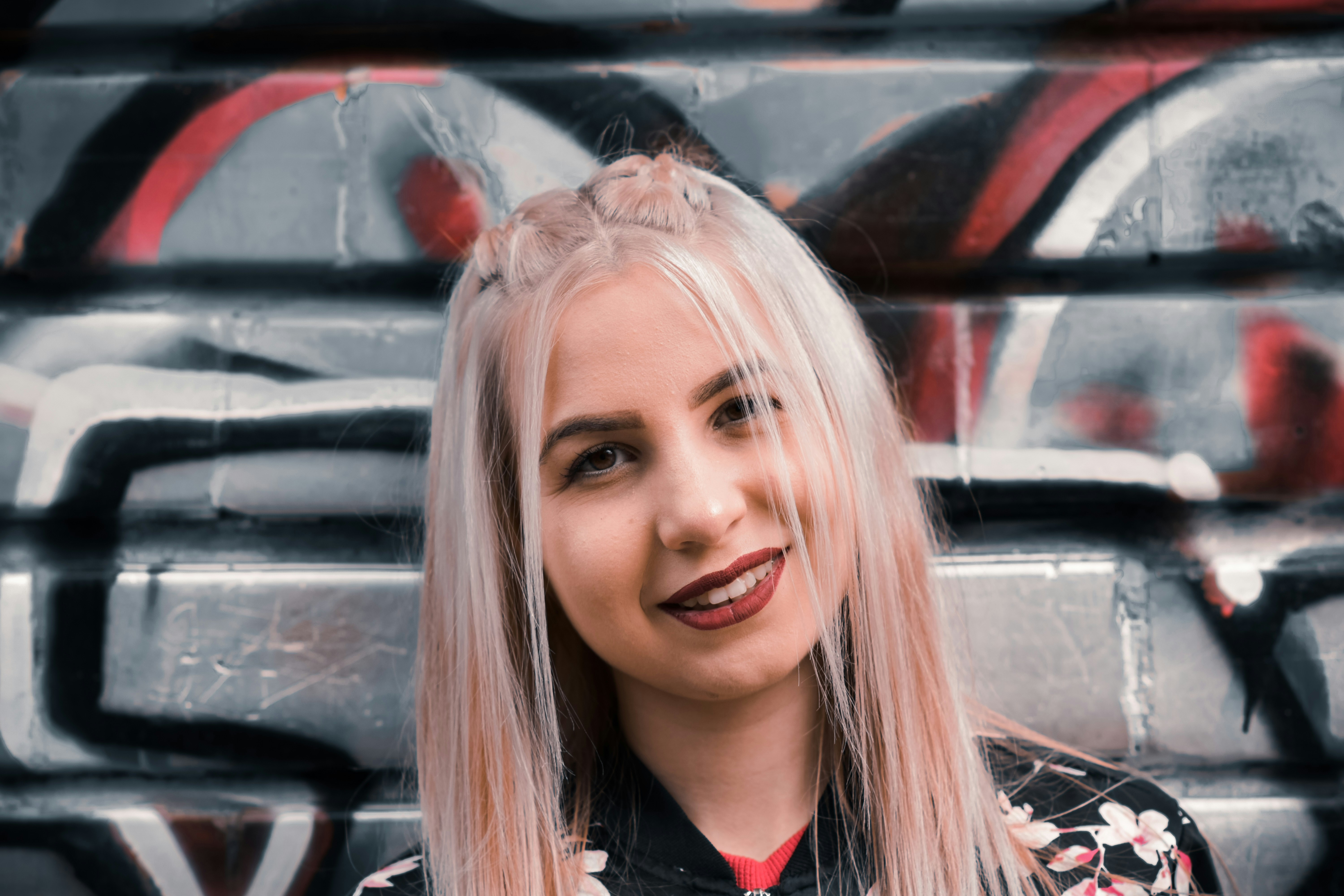 Young woman with long, light hair smiles against a vibrant graffiti backdrop, showcasing urban artistry.