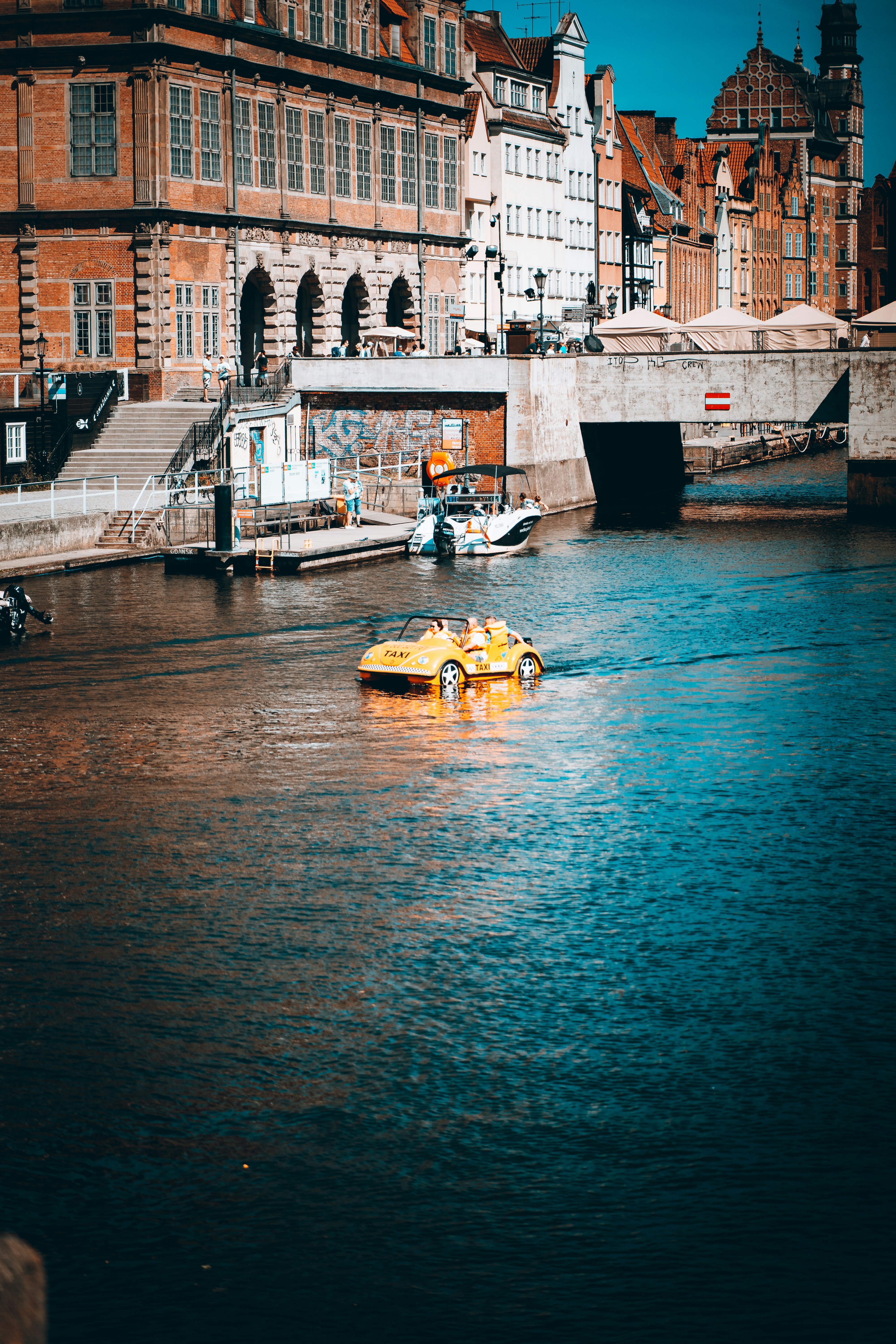 Yellow speedboat gliding past brick warehouses along a sunlit harbor