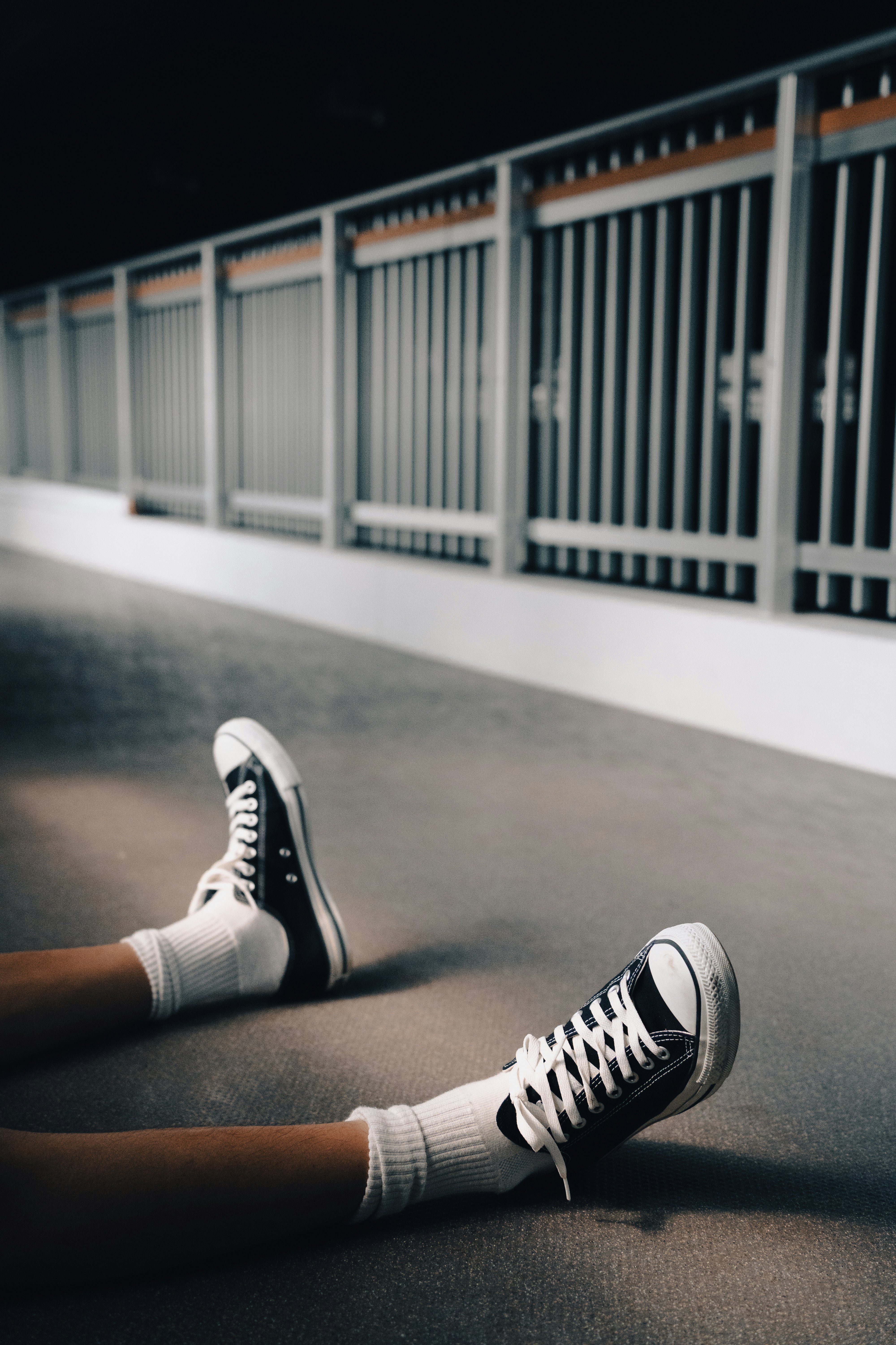 Black and white sneakers resting on a smooth surface, with a blurred railing in the background, evoking a sense of relaxed urban life.