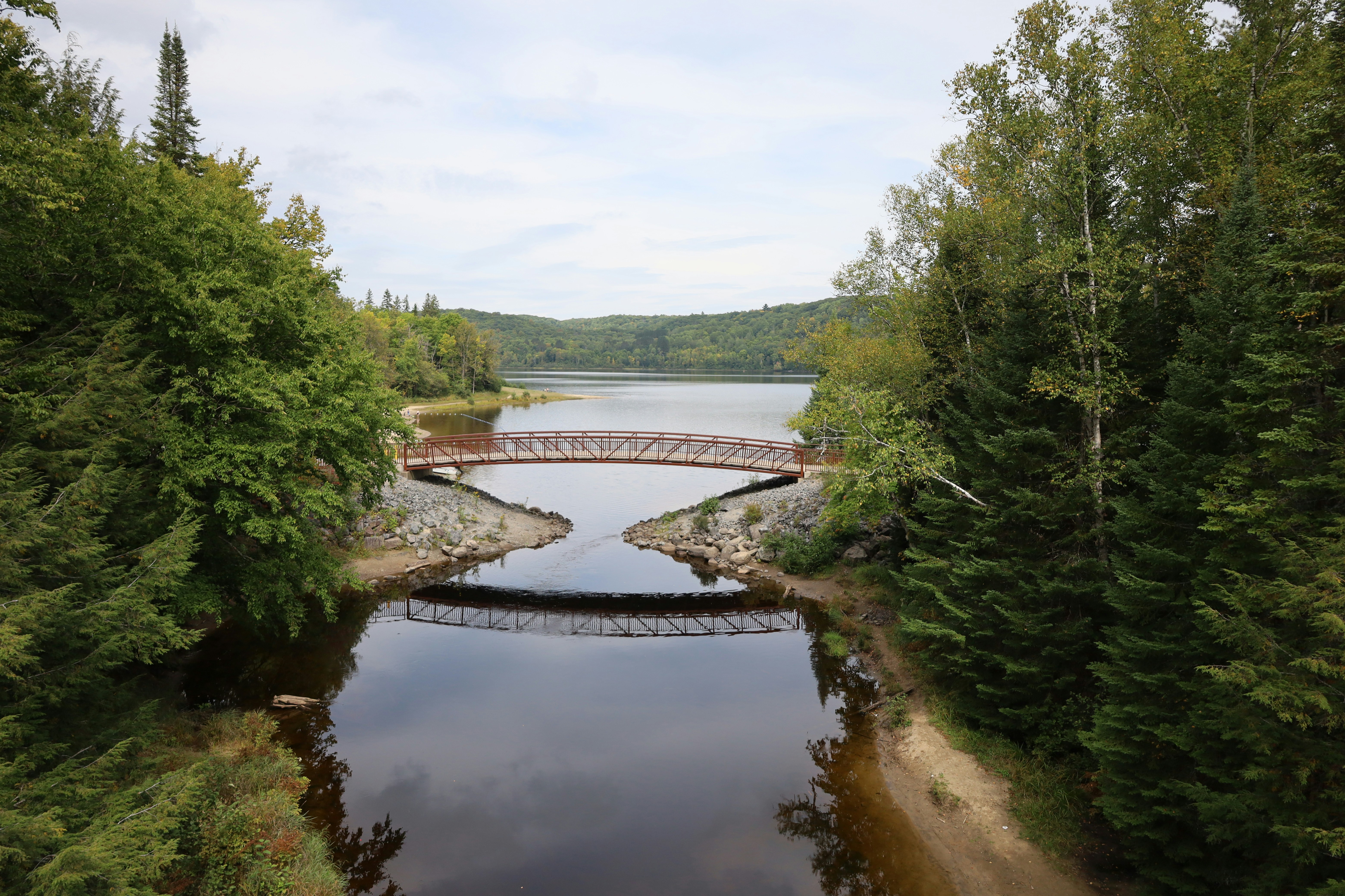 Two wooden bridges span a tranquil lake surrounded by lush greenery and forested hills.