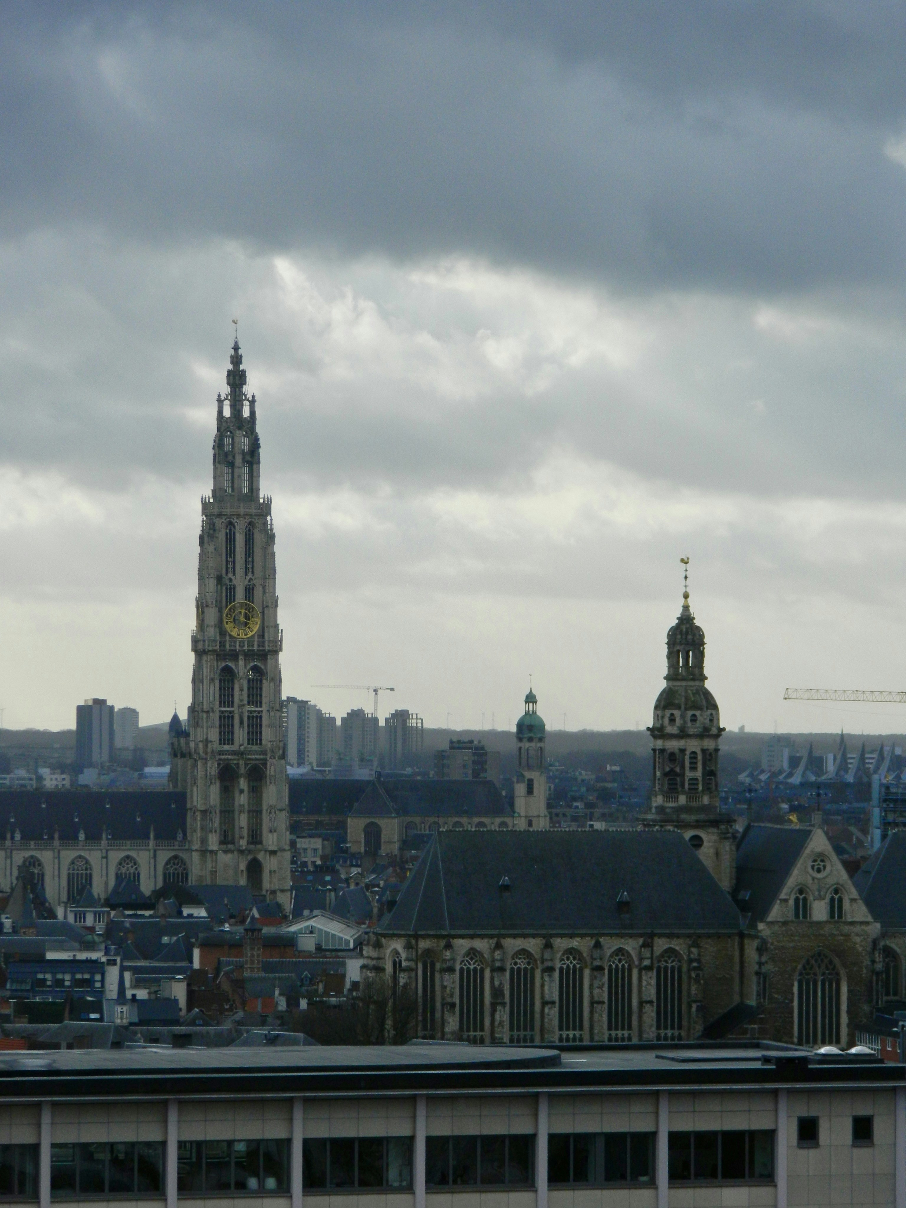 Historic towers rise above the cityscape of Antwerp under a moody sky, showcasing intricate architectural details.