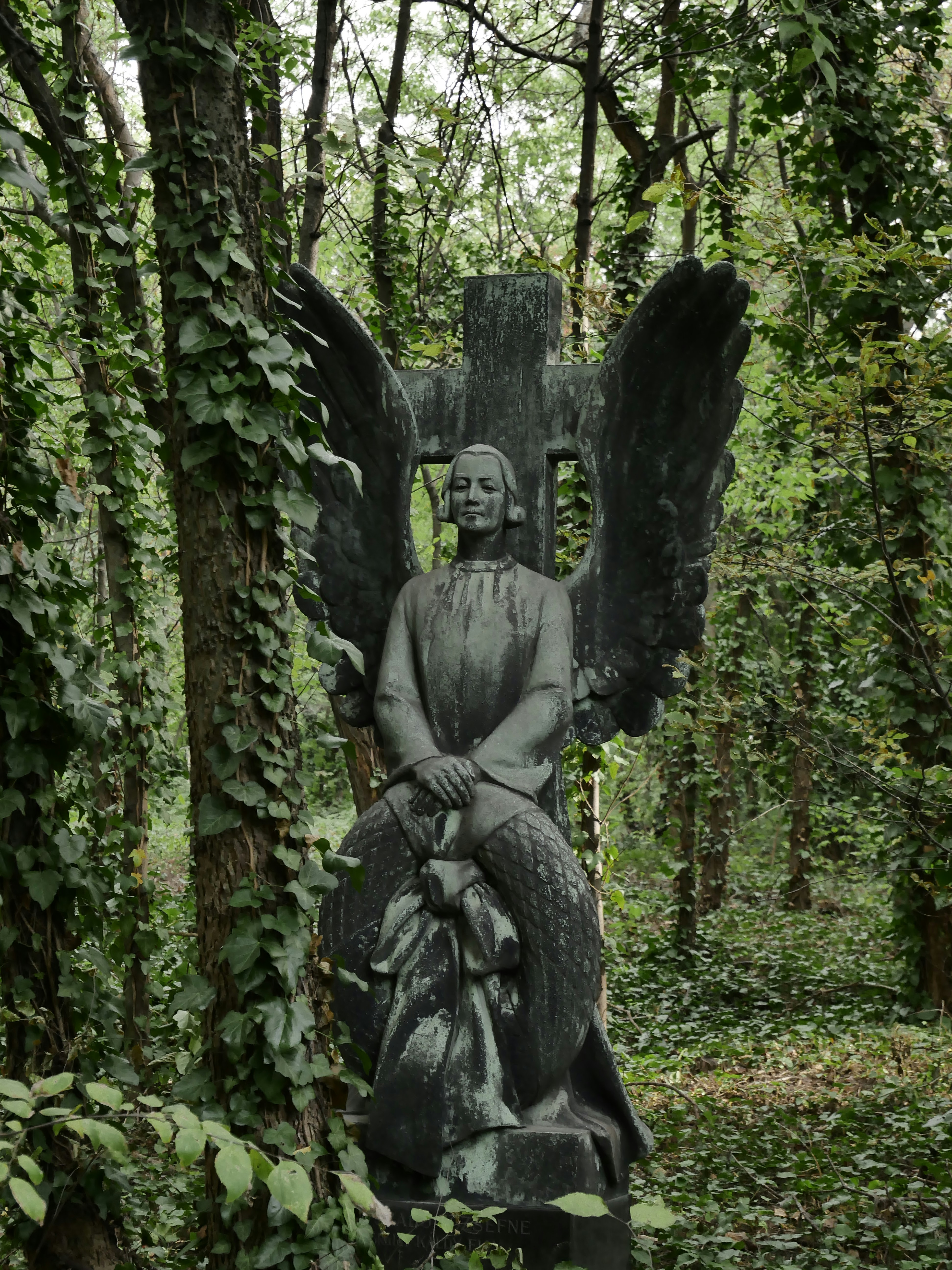 A serene angel statue with outstretched wings sits amidst a lush, overgrown forest, embodying a sense of peace and remembrance.