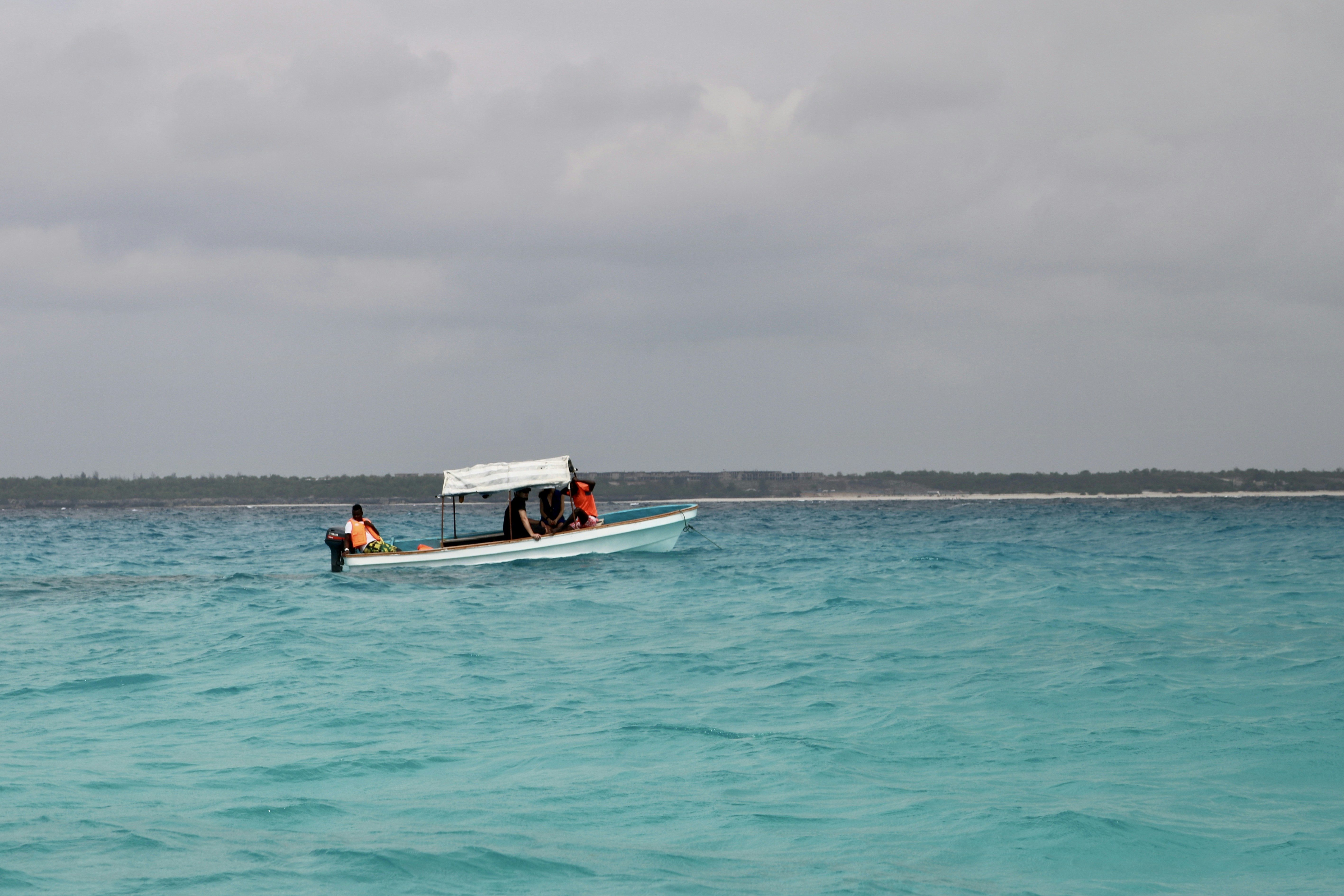 Small boat with passengers navigating clear turquoise sea under a cloudy sky.