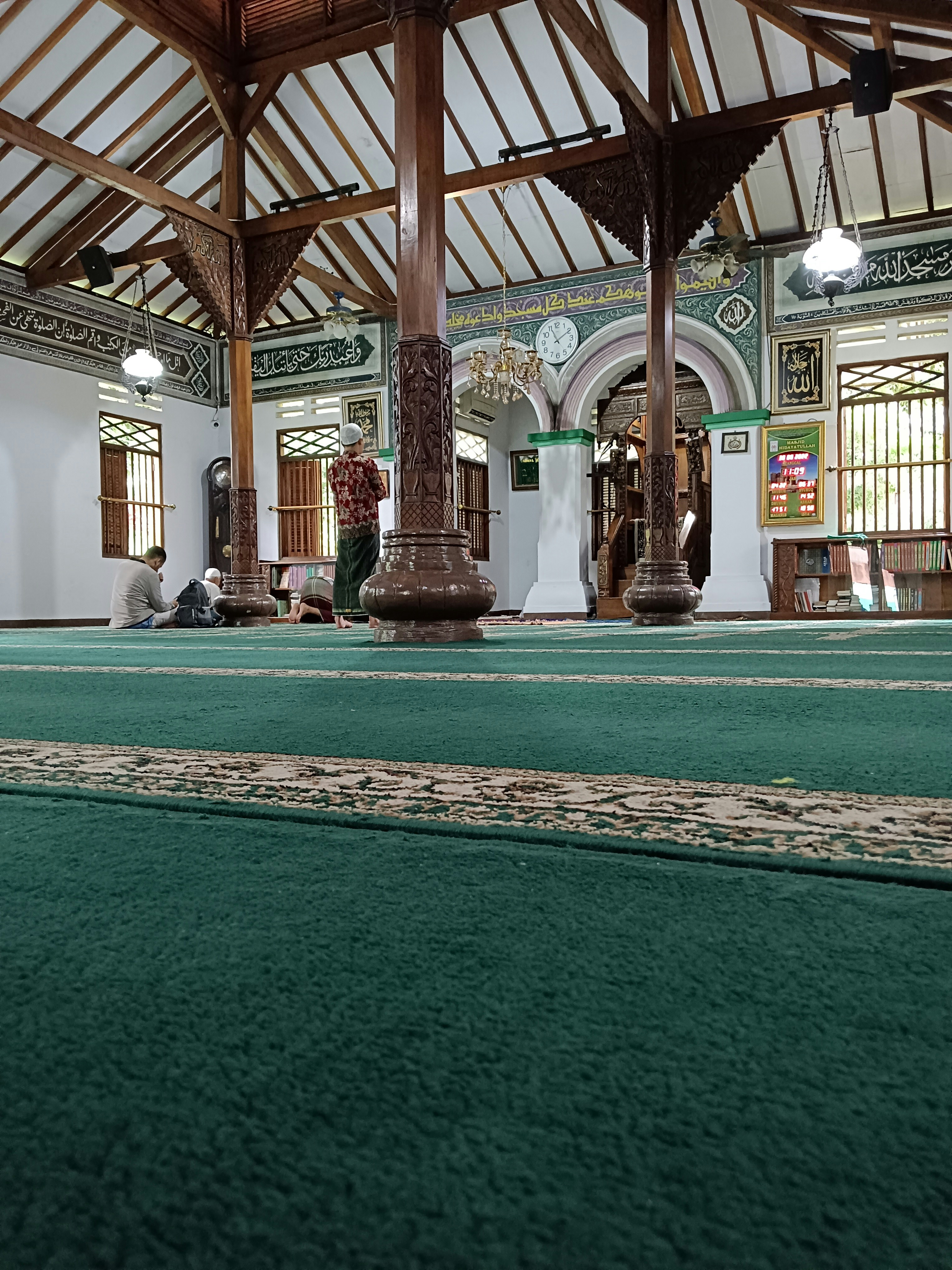 Green Carpeted Prayer Hall with Handsome Wooden Columns and Arched Decor