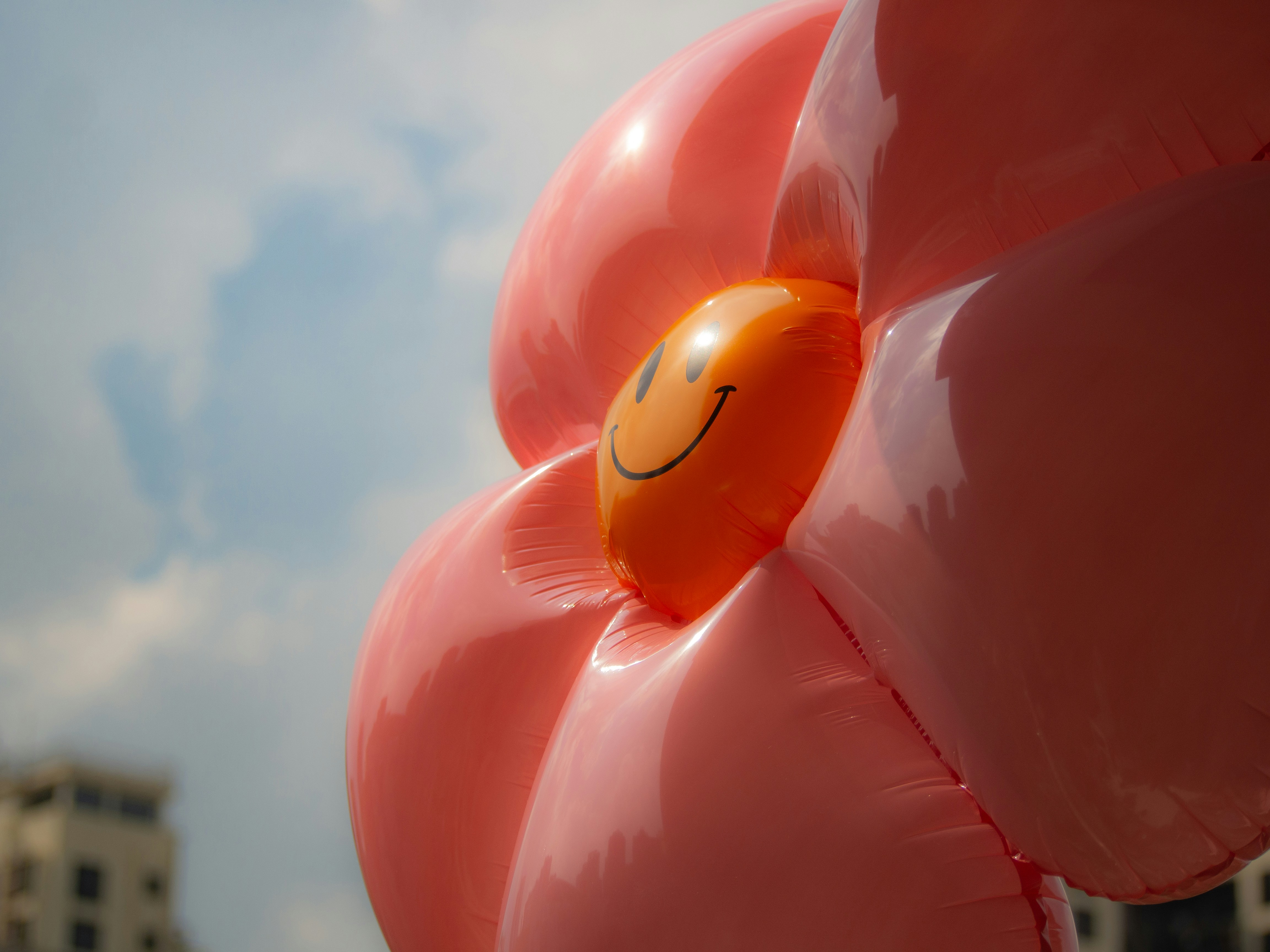 Bright pink balloon shaped like a flower with a smiling face against a cloudy sky.