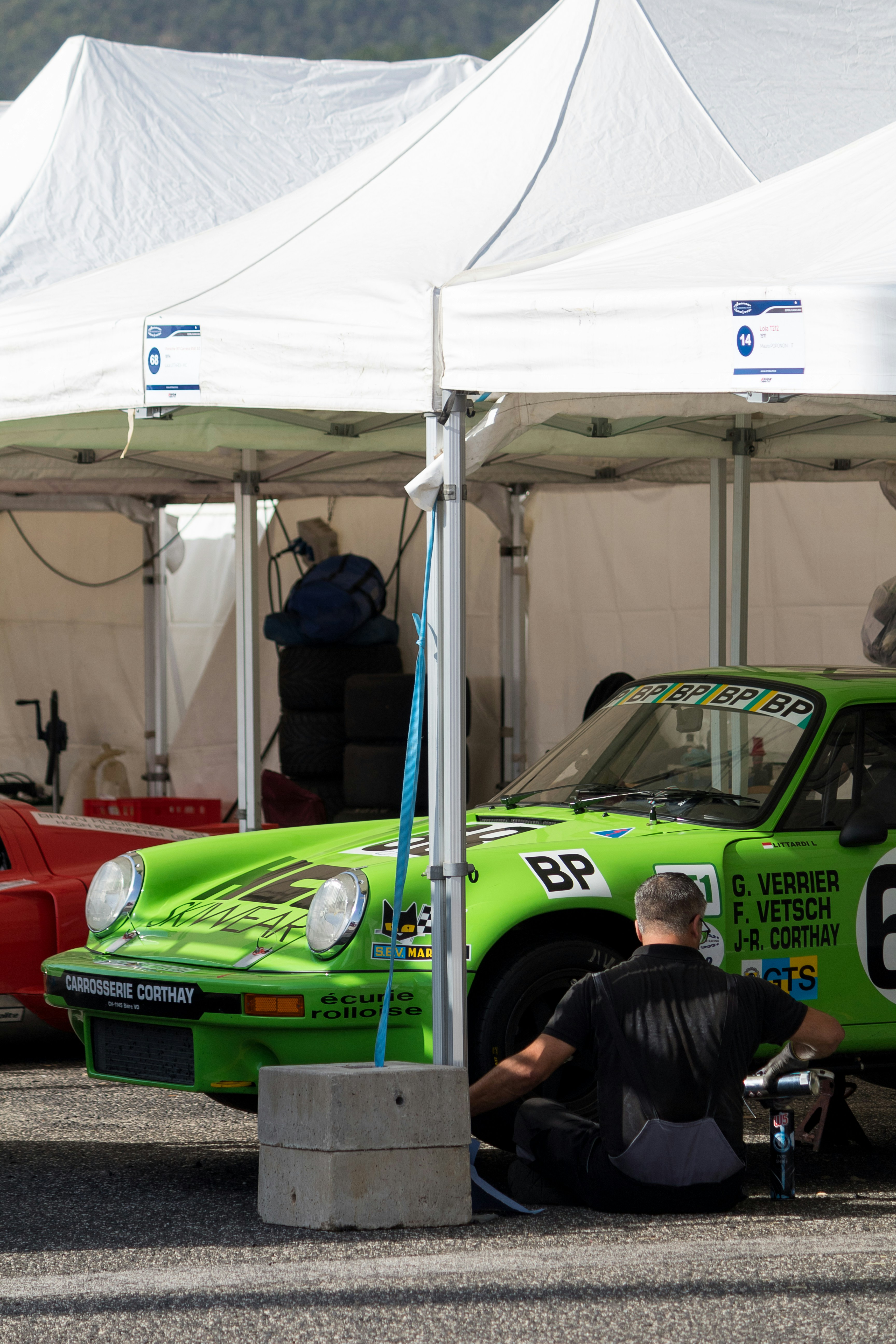 Lime-Green Race Car Under White Pit Tents, Mechanic at the Front Wheel