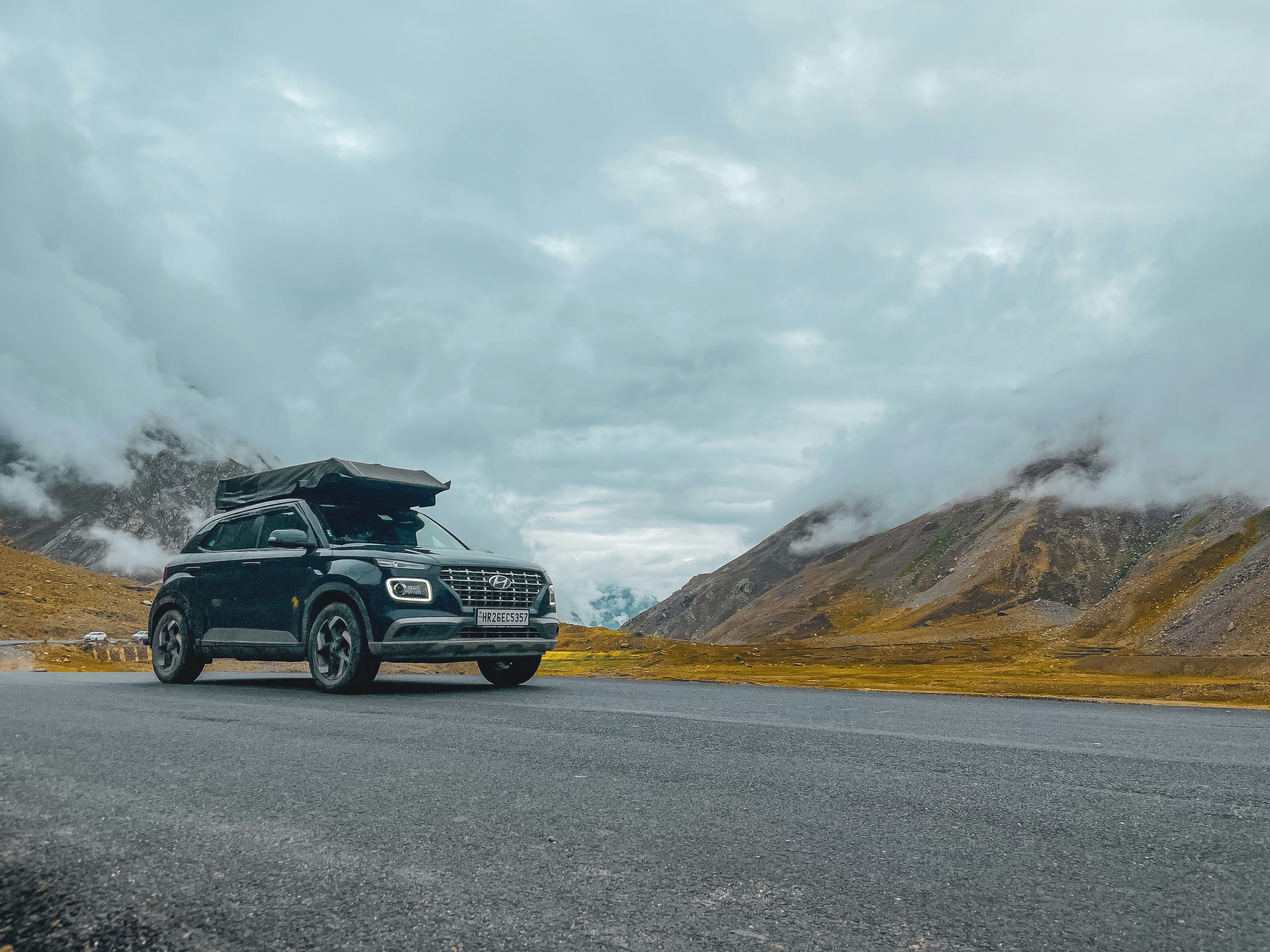 A sleek black SUV parked on a winding road surrounded by dramatic mountains and low-hanging clouds, evoking a sense of adventure.