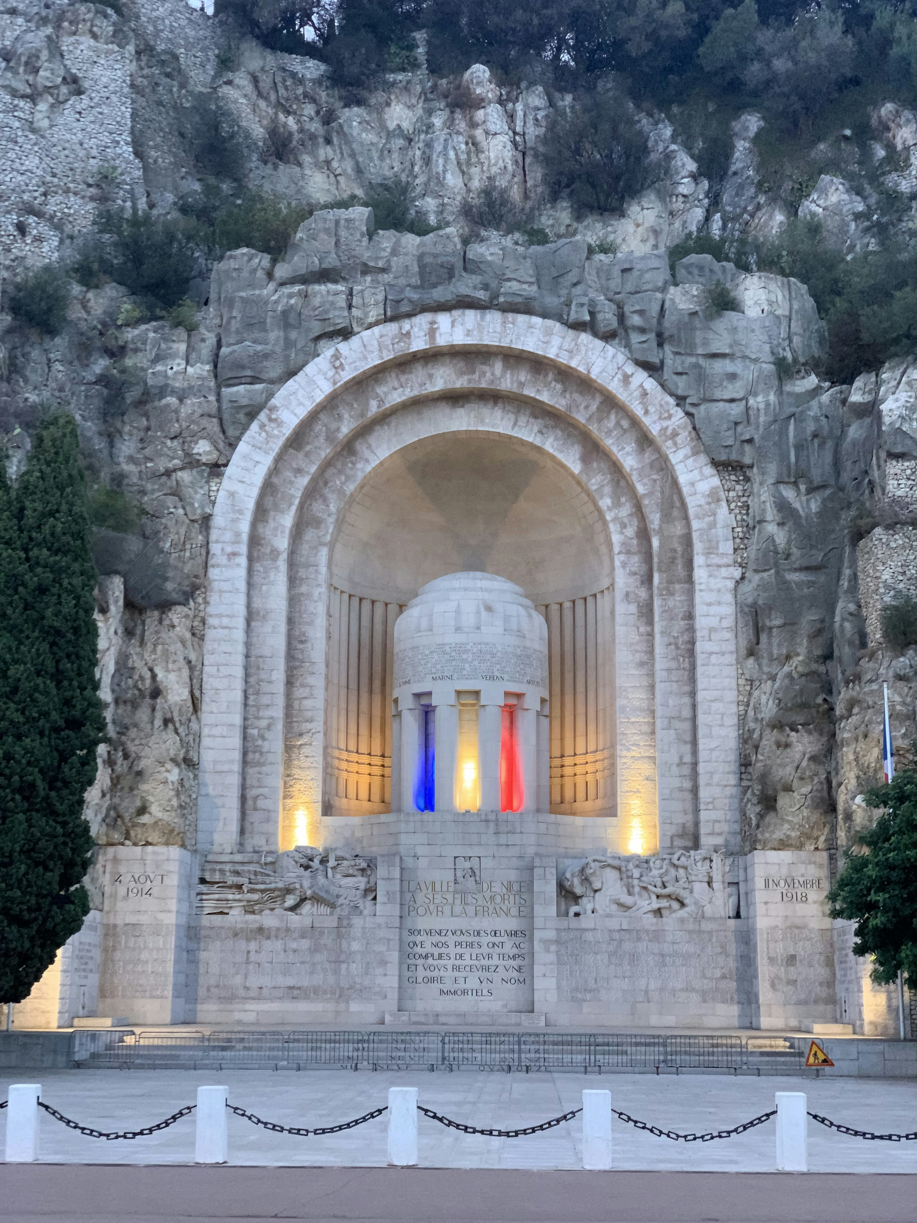 Stone monument embedded in a rocky hillside with French flag colors illuminated at dusk.