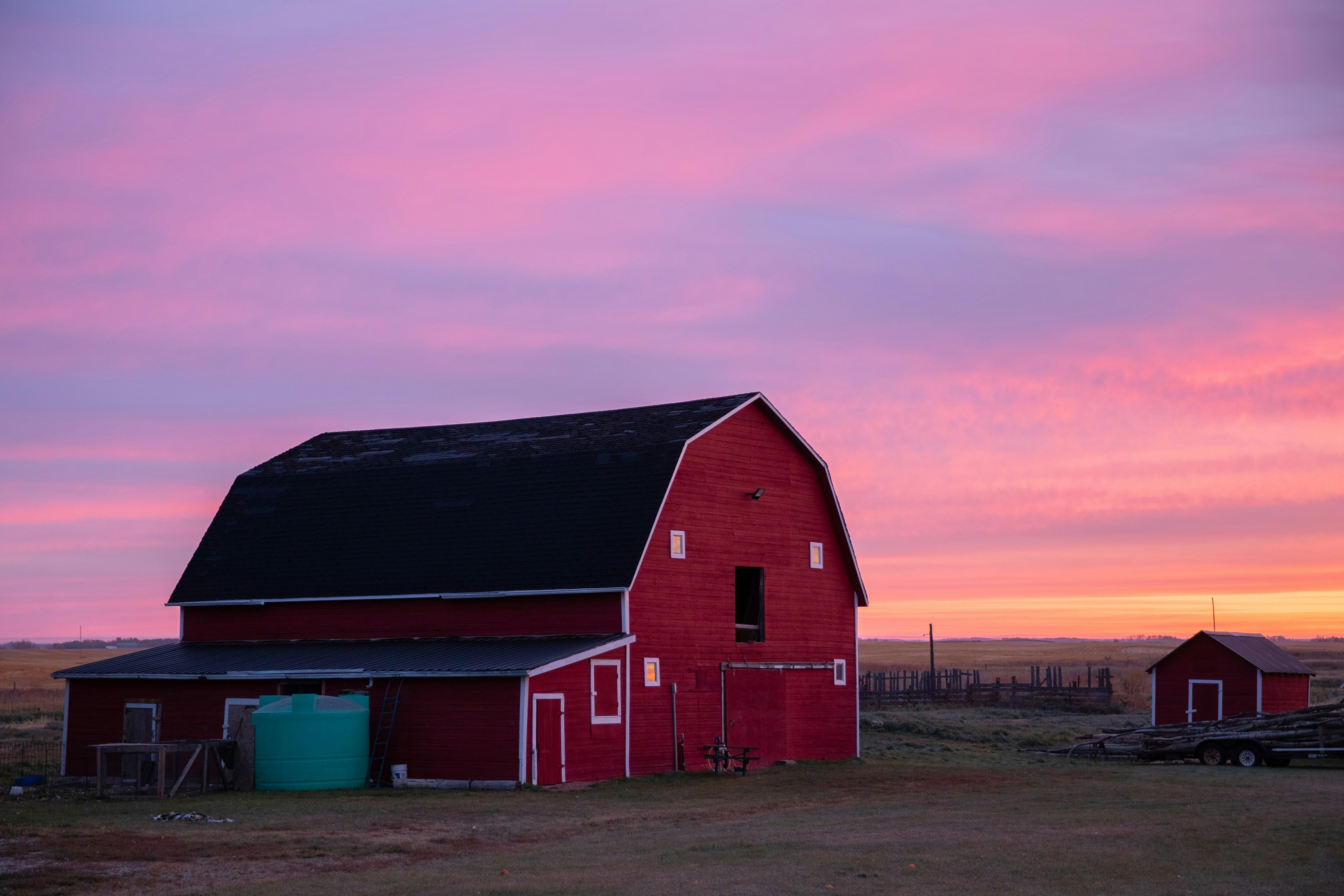 Rustic red barn under a vibrant pink and purple sky at twilight, with a smaller shed nearby.