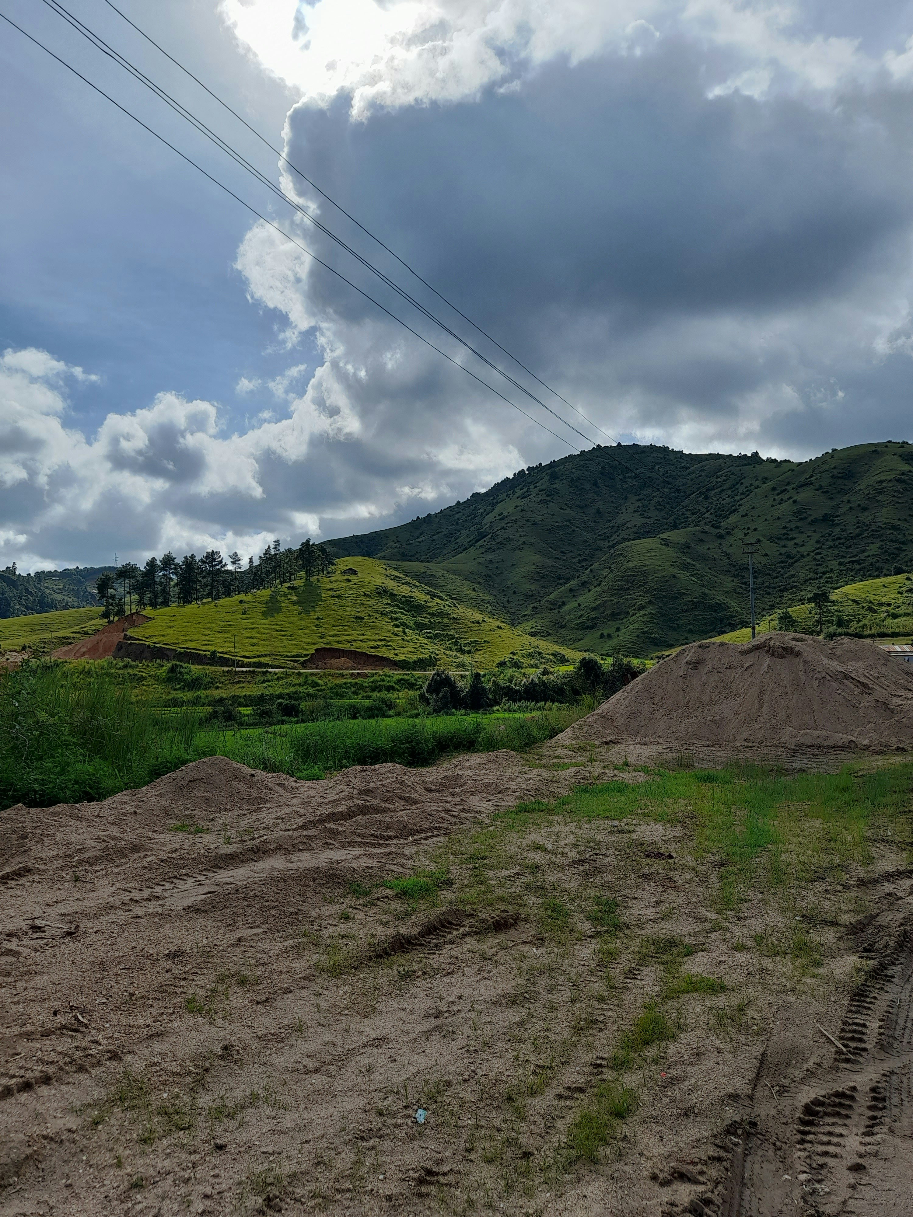 Lush green hills beneath a sky filled with thick, dramatic clouds and overhead power lines.