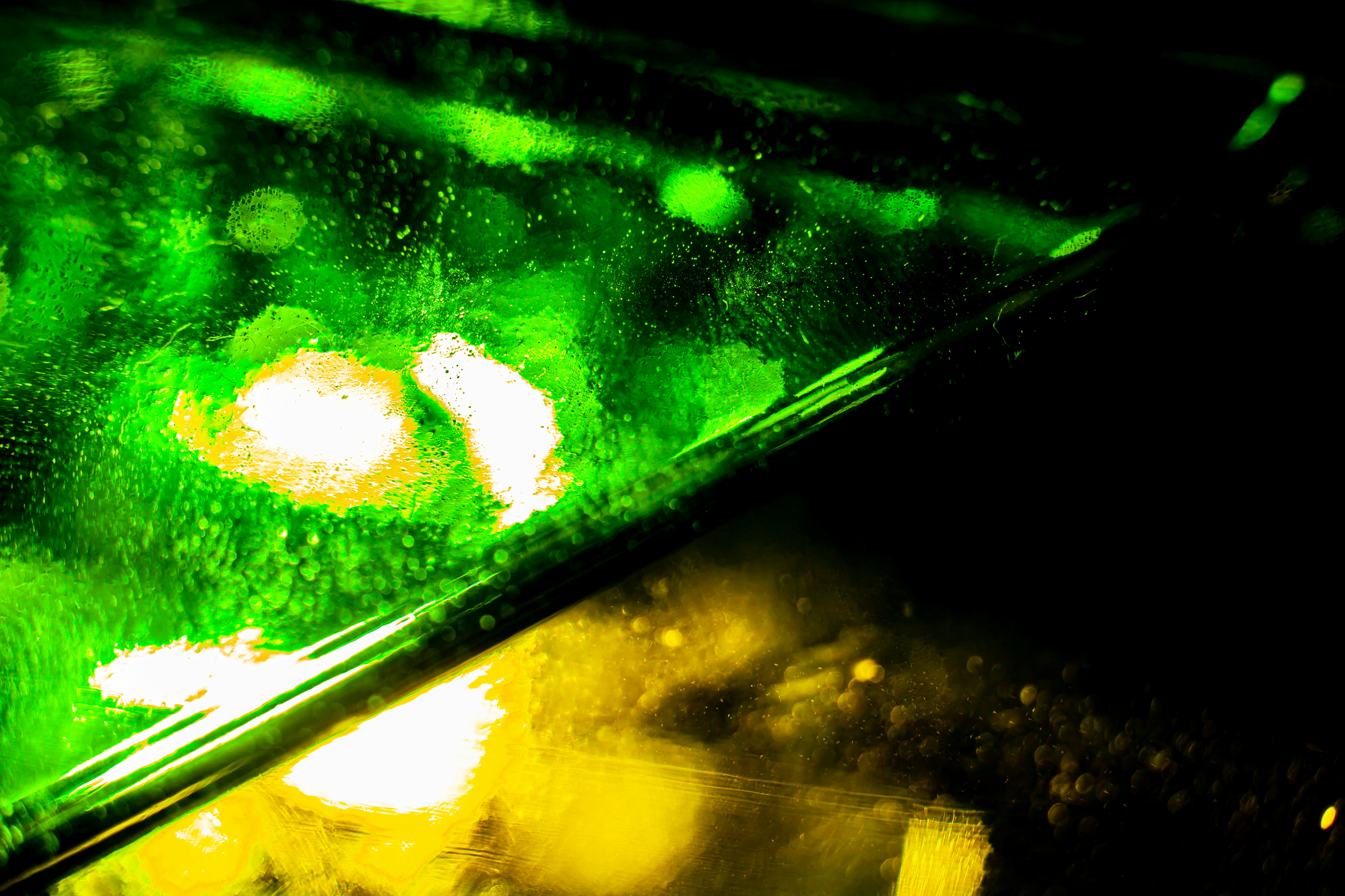 Close-up of vibrant green and yellow light refracting through a glass surface, creating a mesmerizing display of colors and textures.