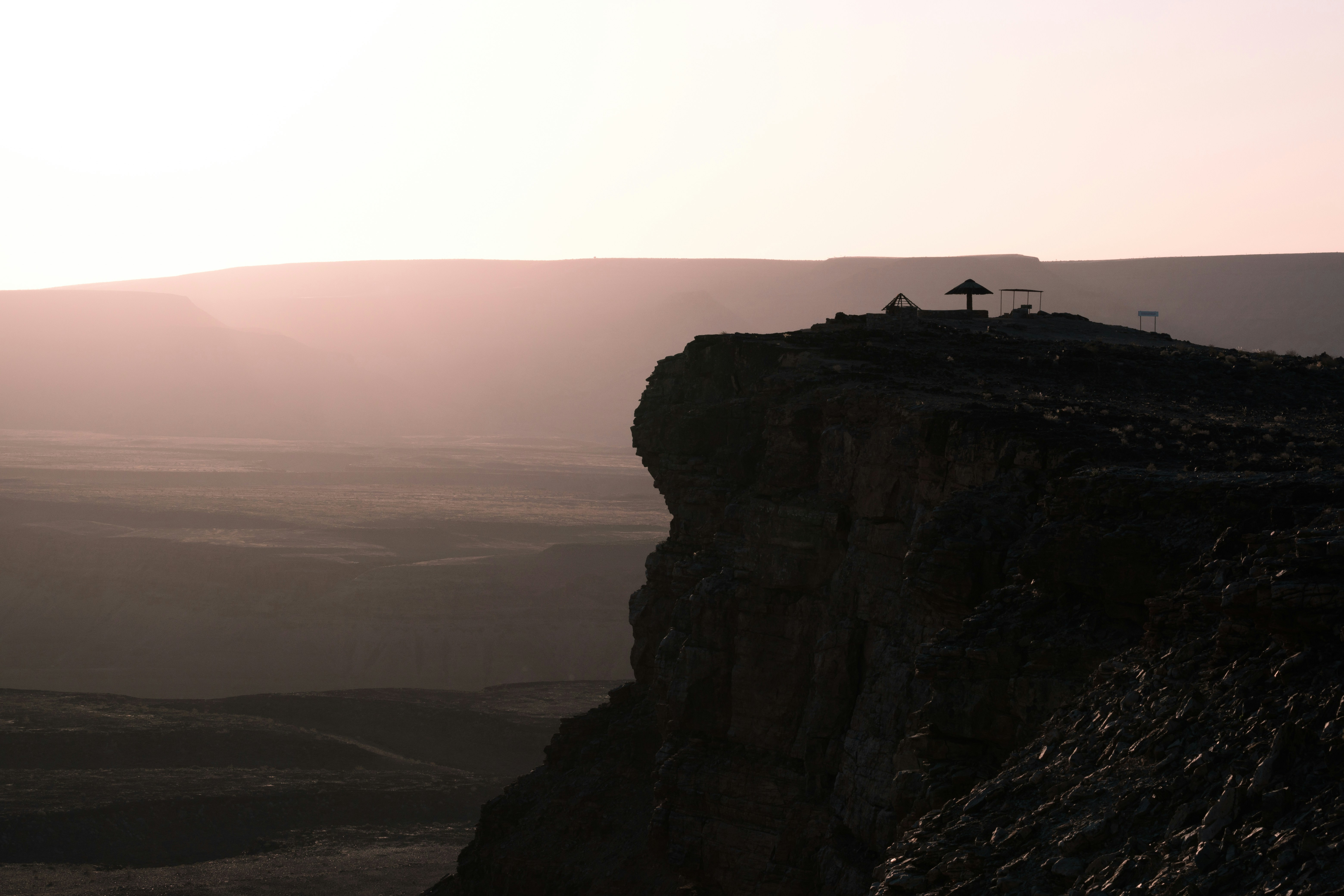 Silhouetted tree on a rocky cliff at sunrise, overlooking a vast canyon landscape.